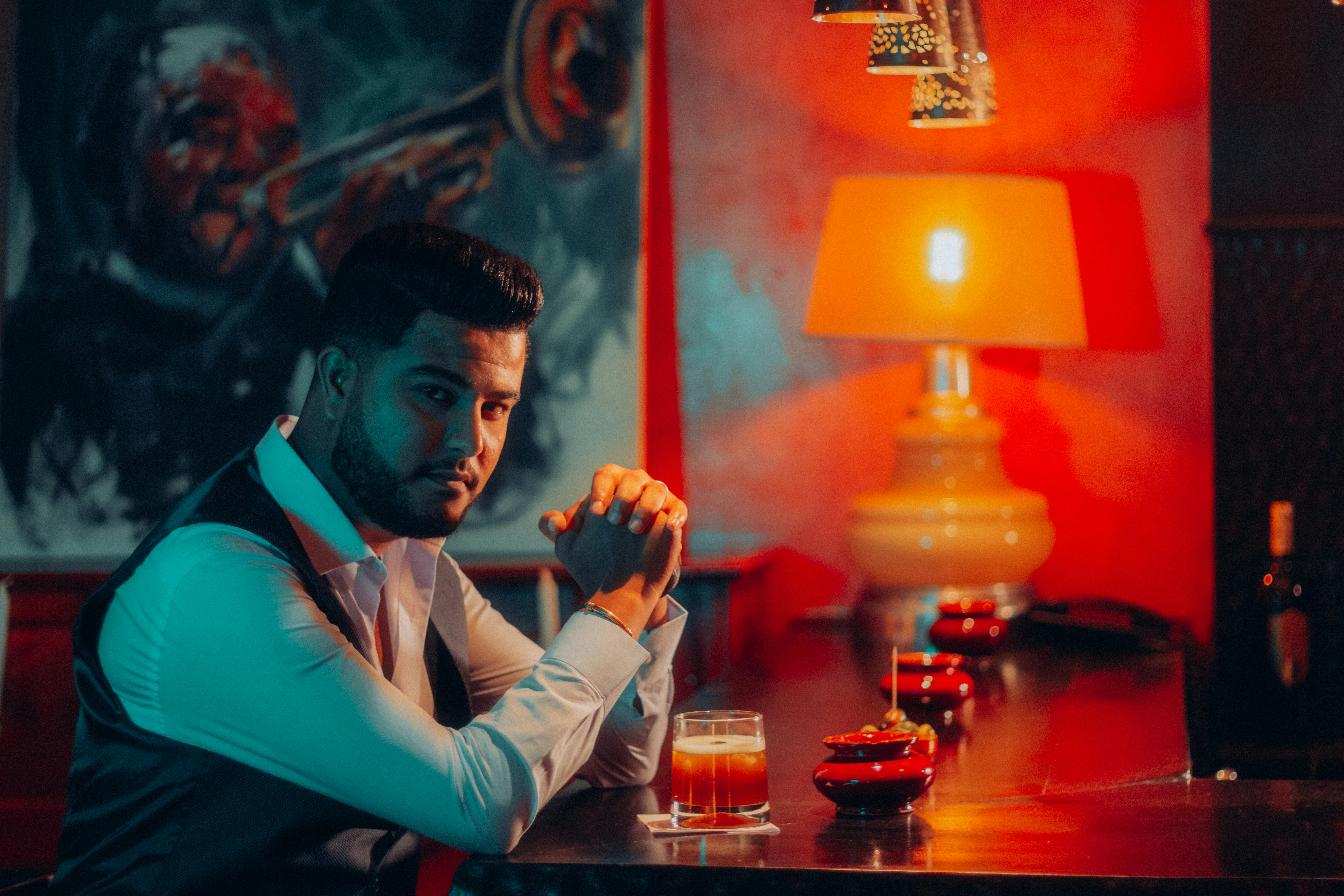 Man sitting at a dimly lit bar with a warm lamp glow and jazz mural in the background.