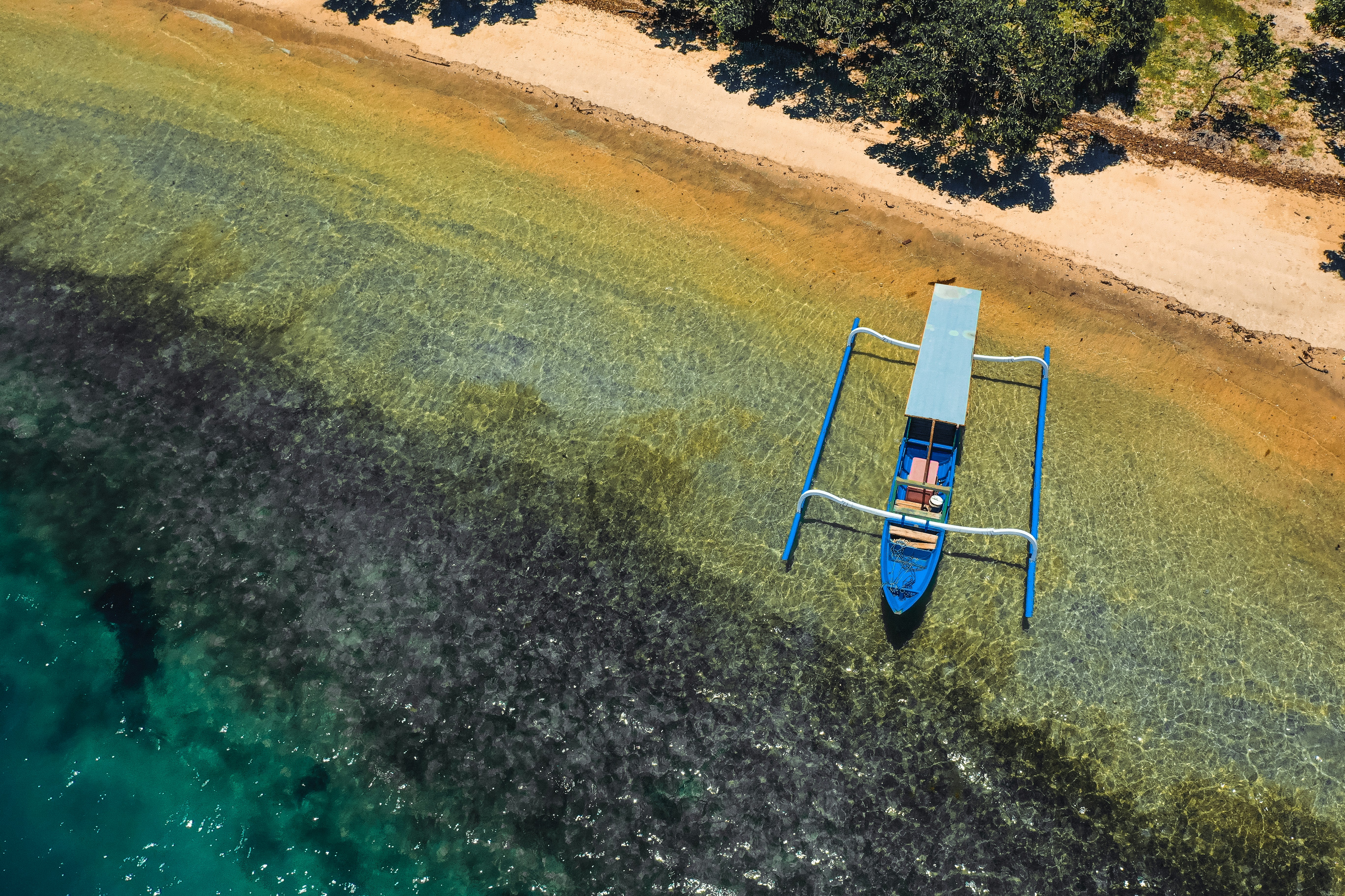 Blue Outrigger on Turquoise Verge: Aerial View of a Quiet Shore