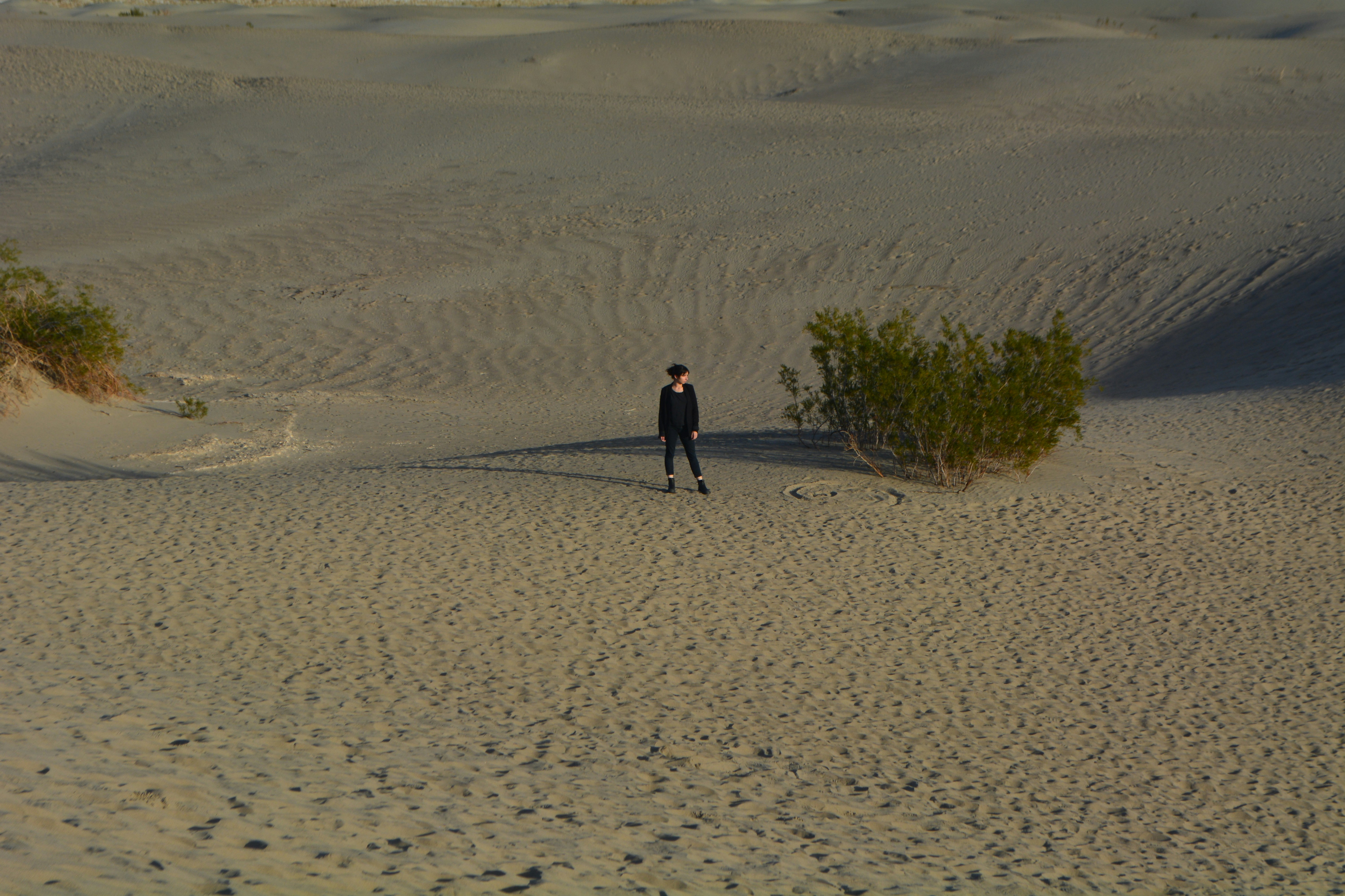 woman in black dress walking on sand during daytime