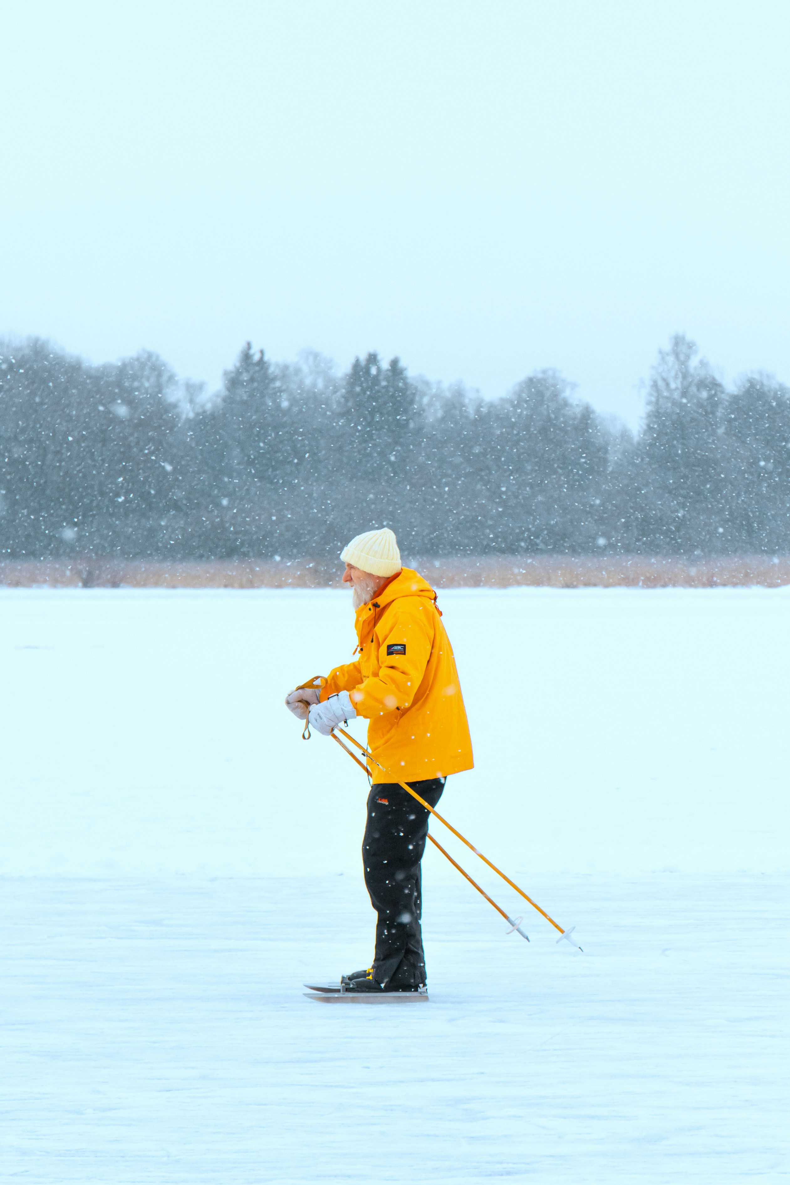 A person in a bright yellow jacket skis across a snow-covered landscape, surrounded by softly falling snowflakes and distant trees.