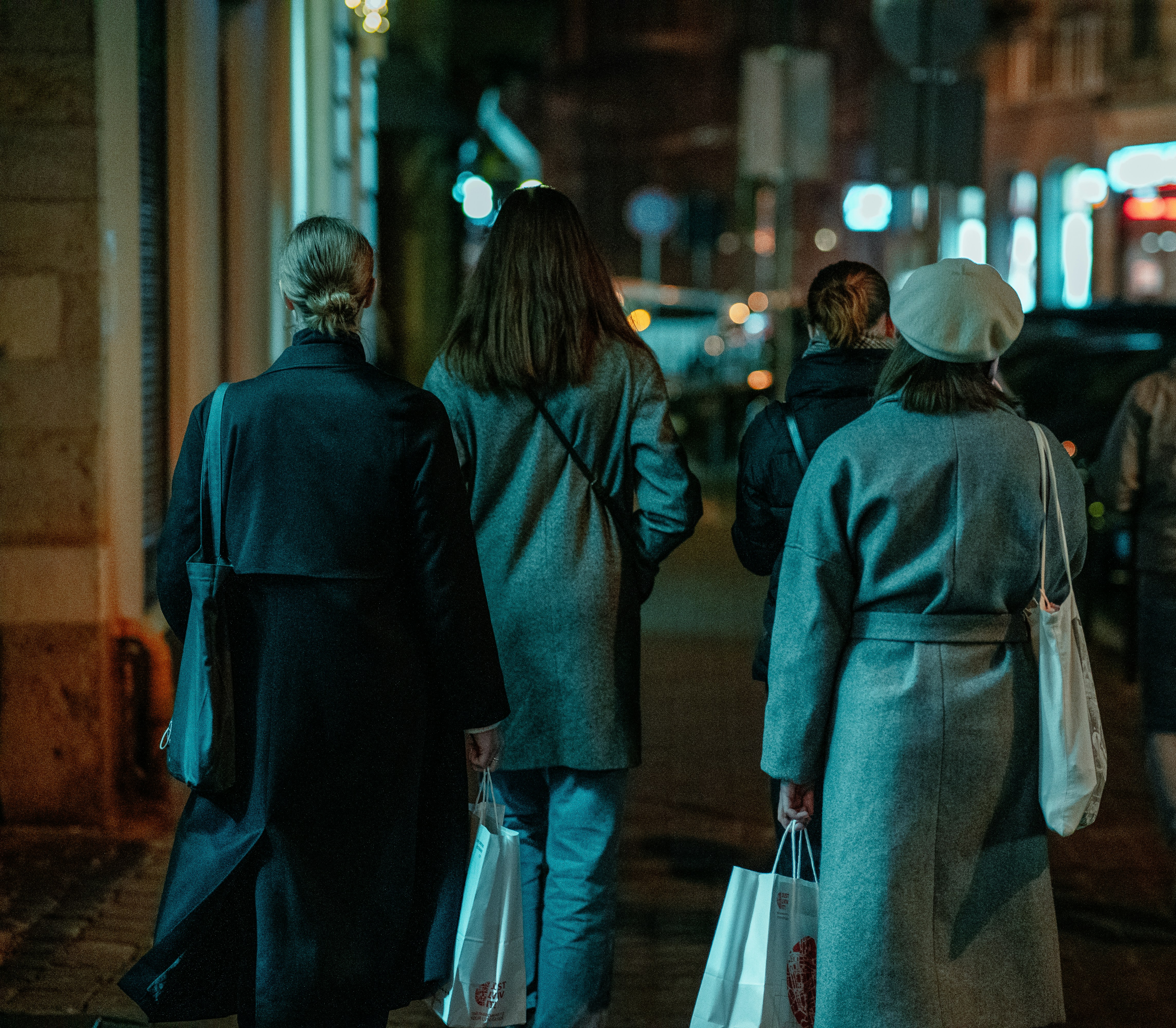 Group of women walking together on a city street at night, each carrying shopping bags. The scene captures the essence of urban life and camaraderie.