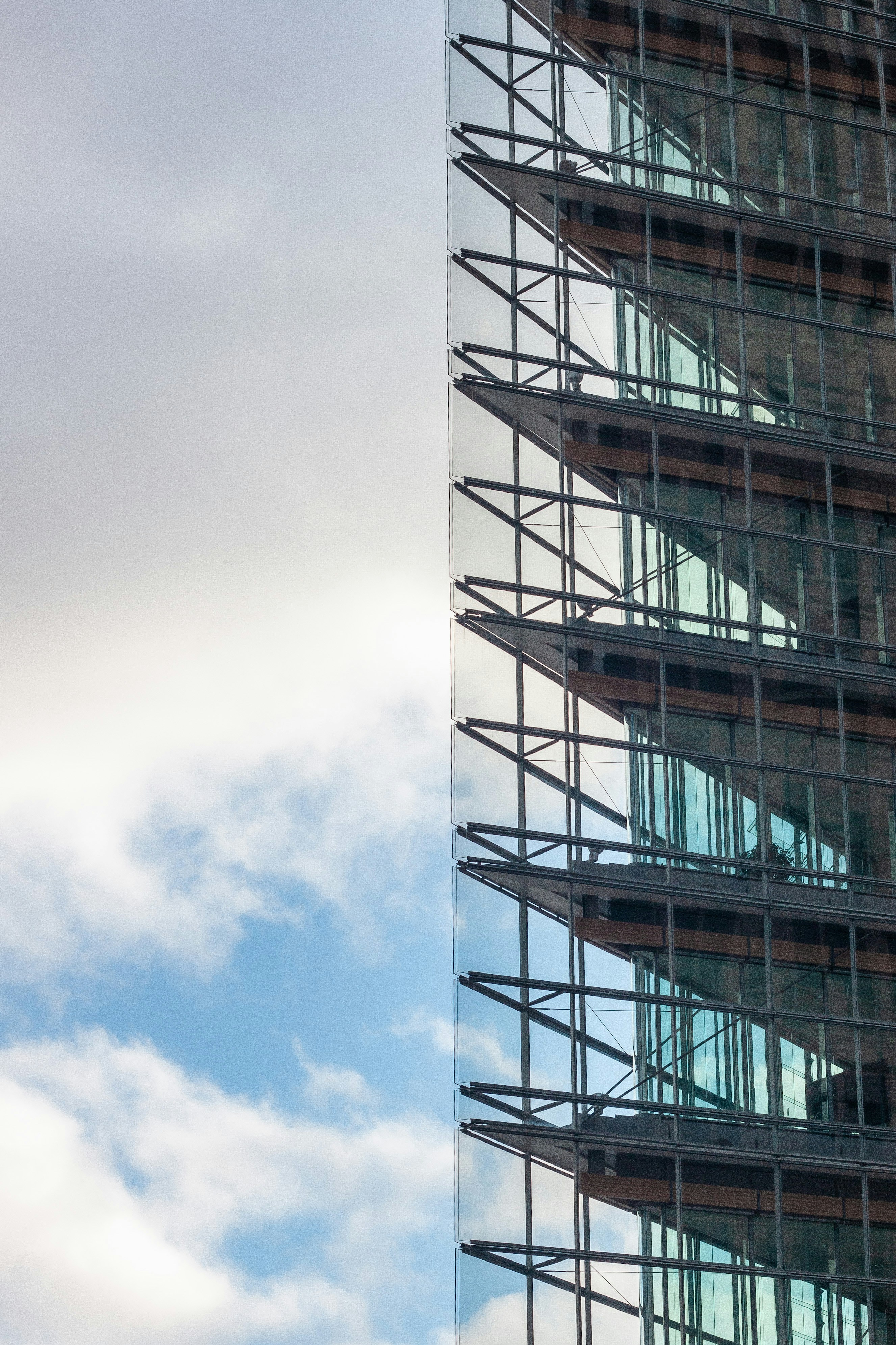 Glass facade of a contemporary building reflecting the sky and surrounding structures, showcasing intricate steel frameworks.