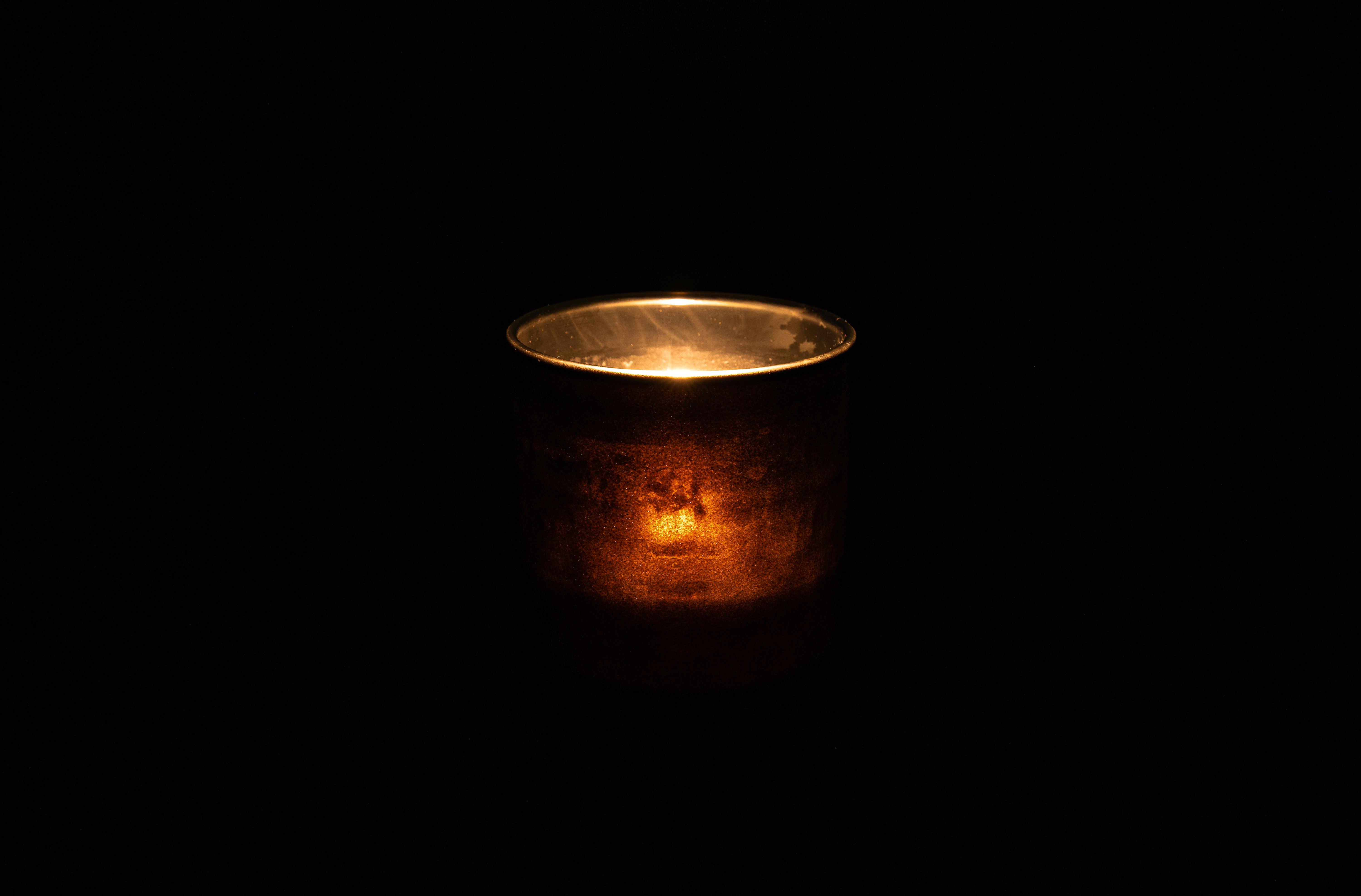 A warm candle flickers softly in a dark setting, casting a gentle glow. The subtle reflections around the flame enhance the tranquil atmosphere.