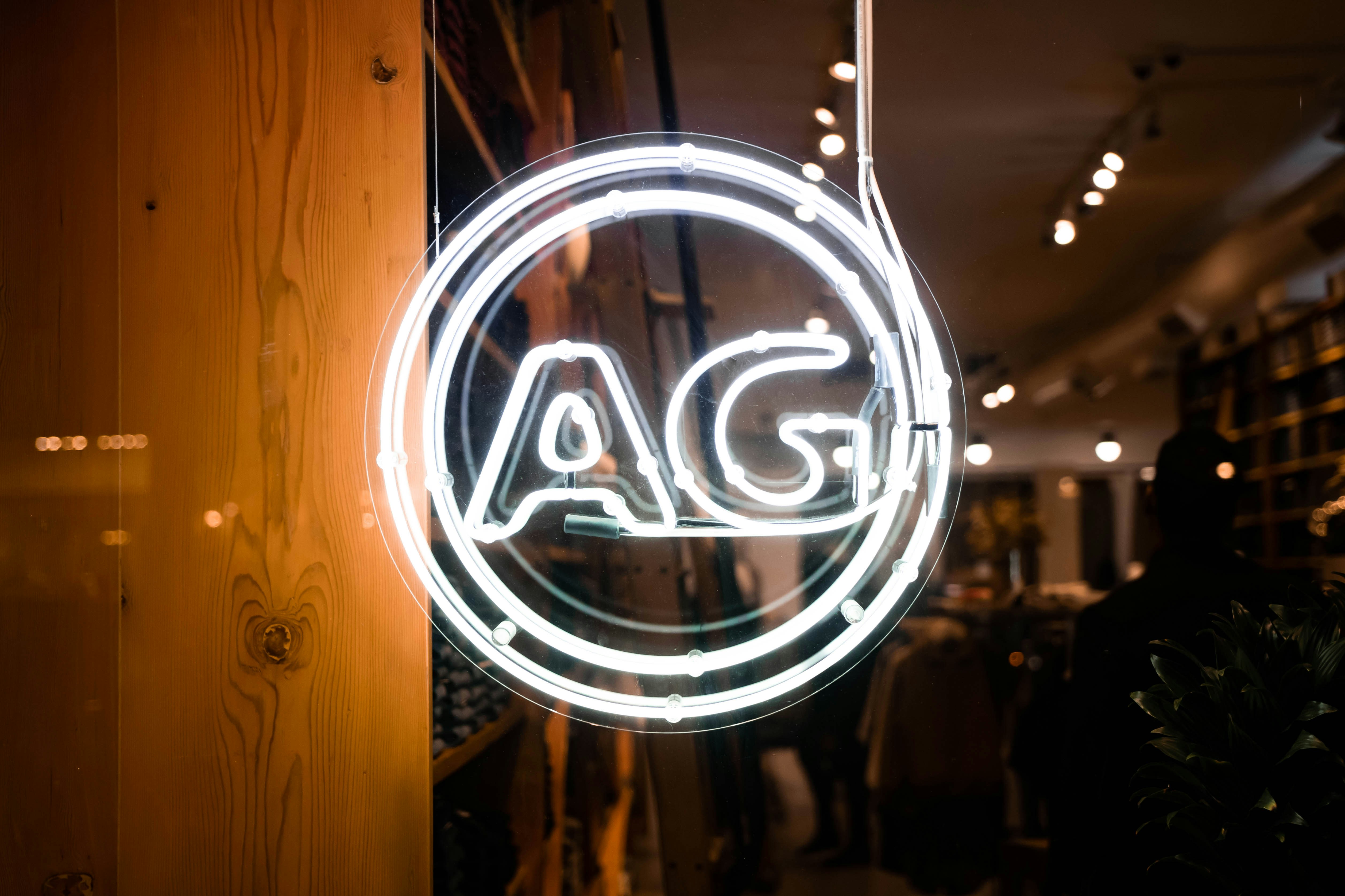 Illuminated neon logo 'AG' against a wooden backdrop in a trendy retail space, showcasing modern branding.