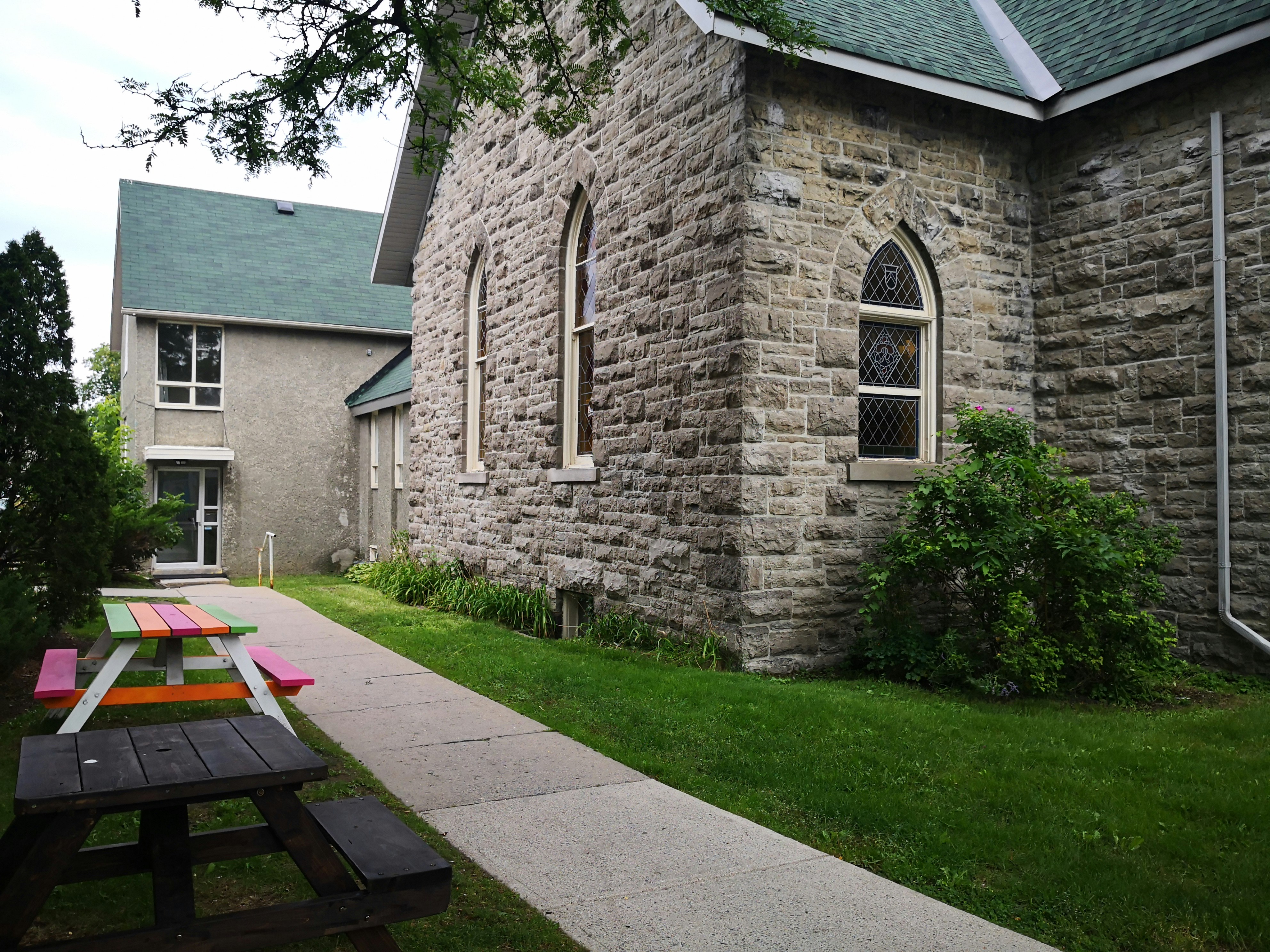 Stone building with arched windows beside a grassy area and colorful picnic tables.