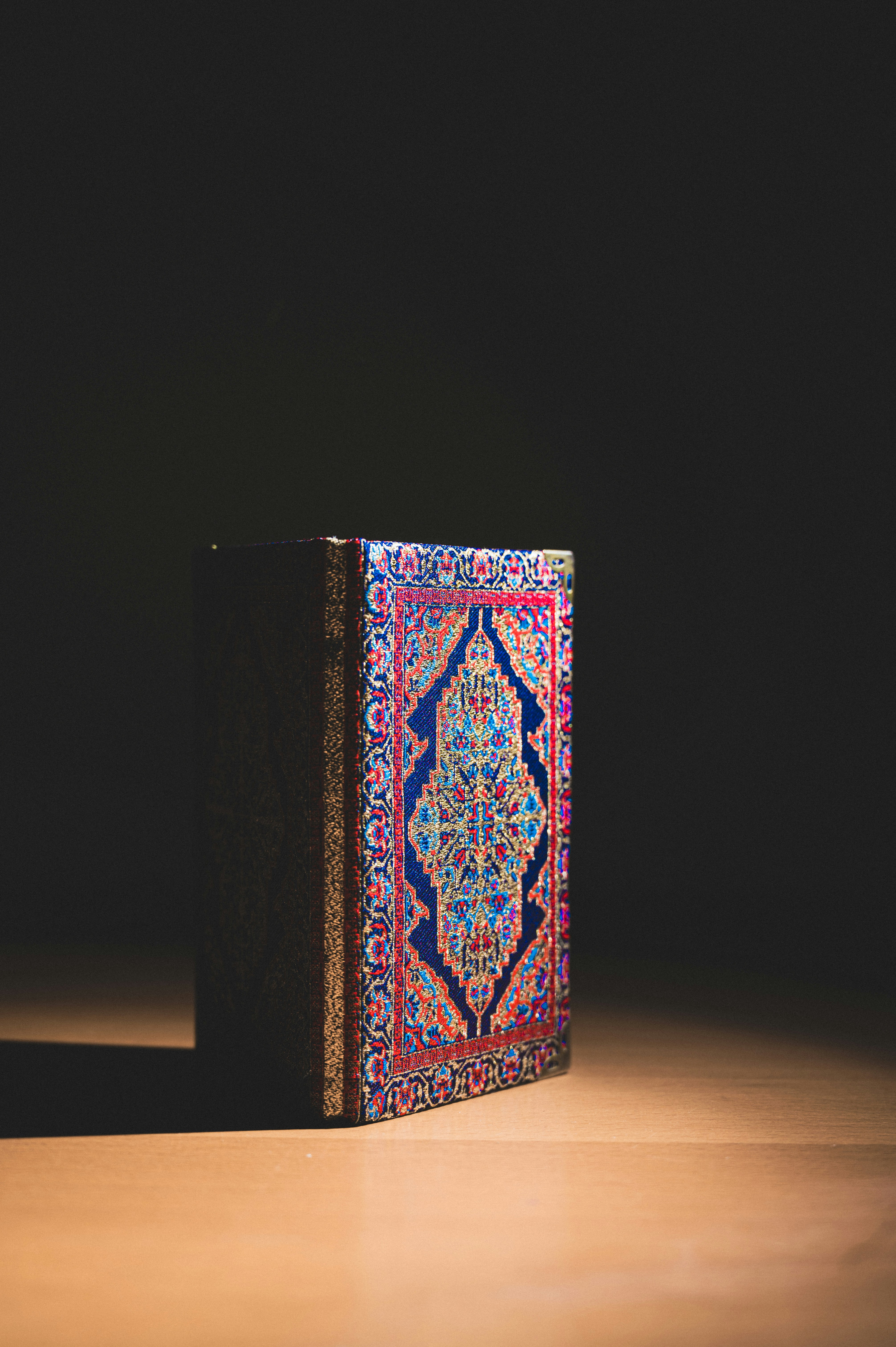 Intricately designed book with vibrant patterns illuminated against a dark background. The craftsmanship showcases traditional artistry.
