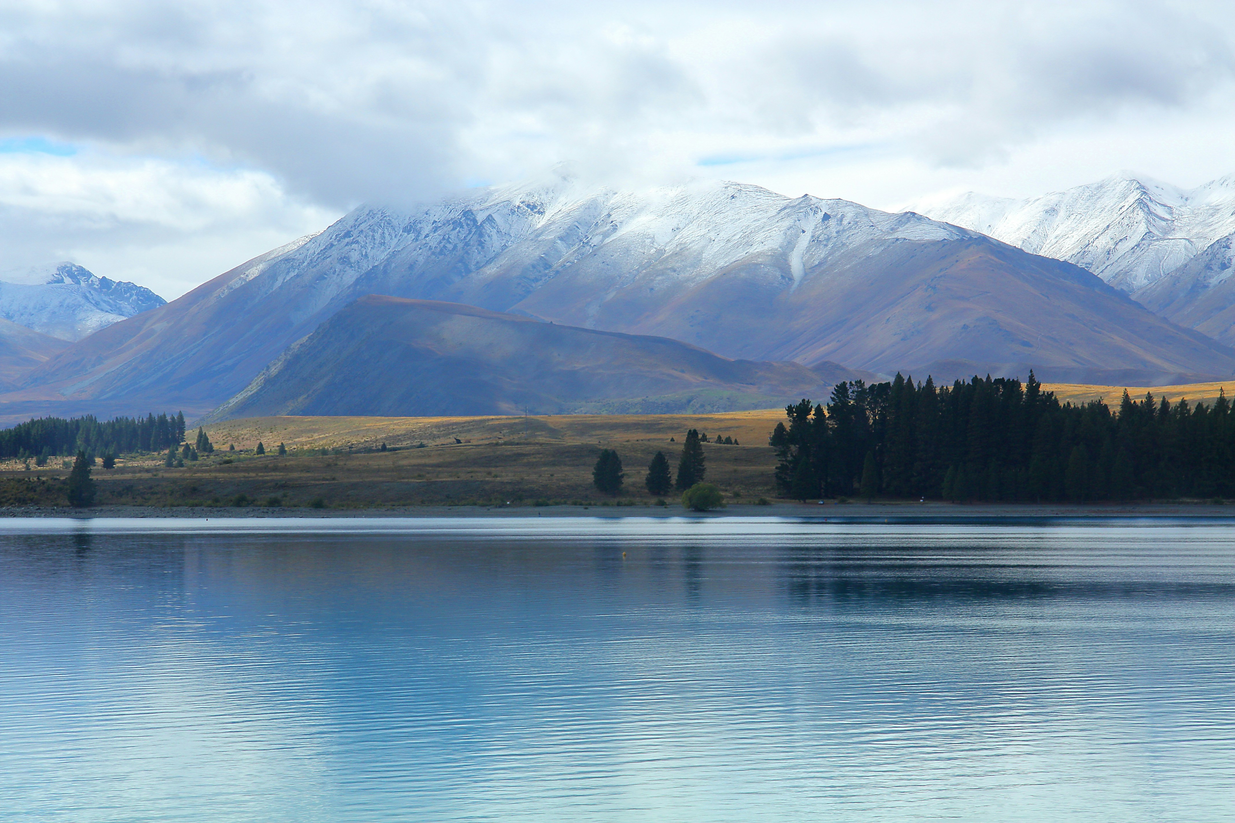 Tranquil lake reflecting snow-capped mountains under a cloudy sky, showcasing the harmony of nature.