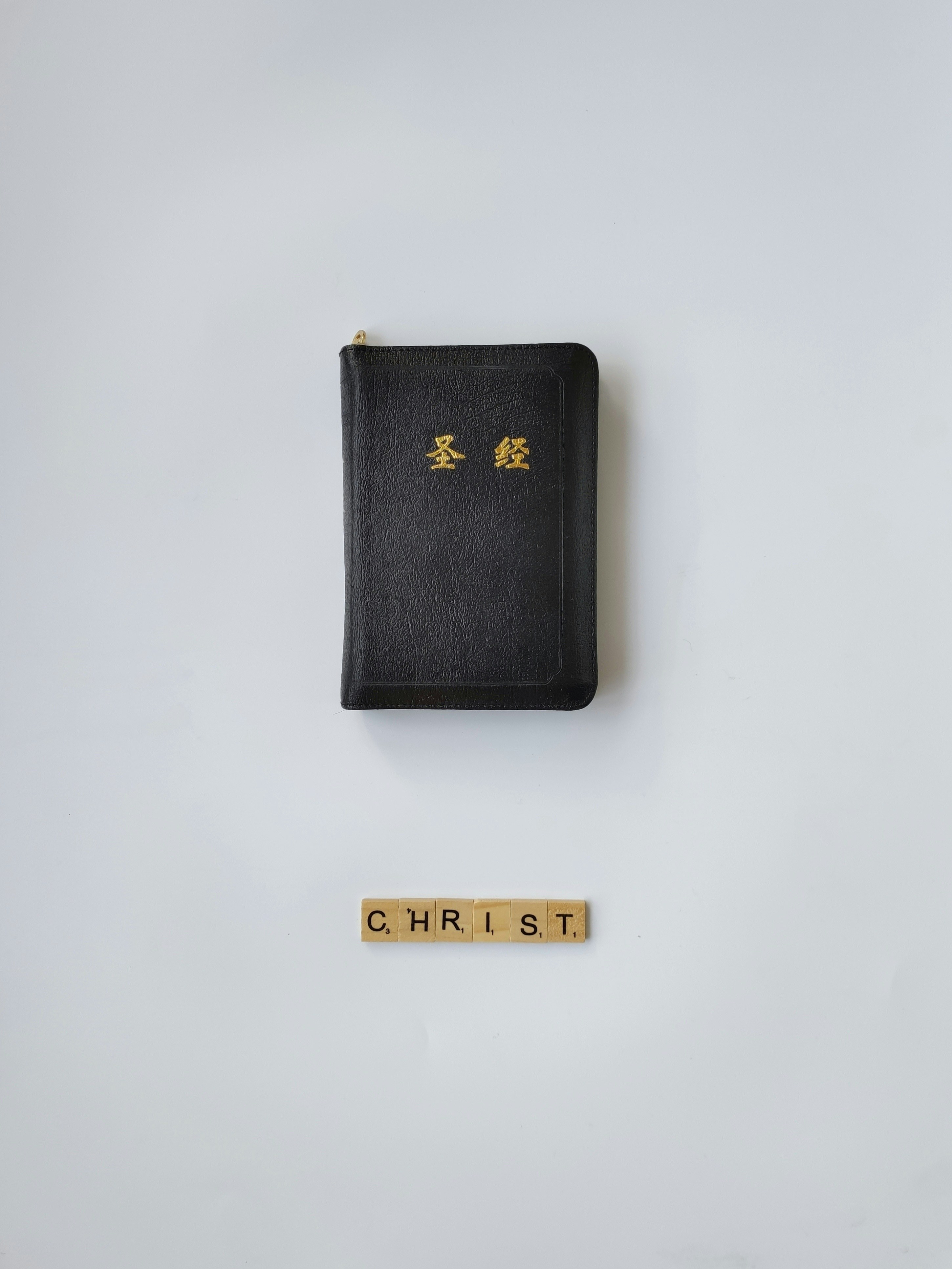 Tiny Gospel: A black Bible and Scrabble letters spelling CHRI ST on a stark white backdrop