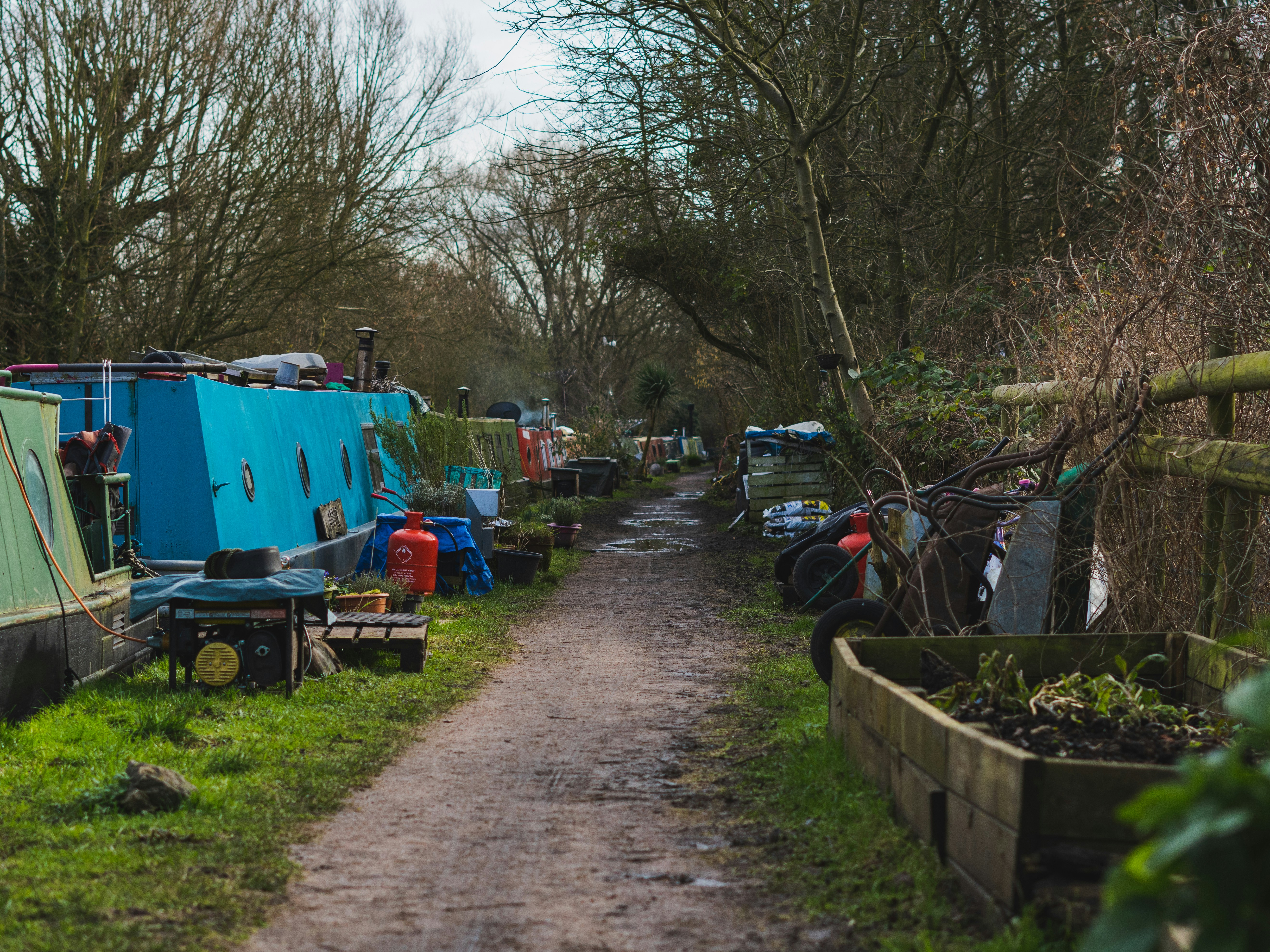 A narrow pathway lined with colorful houseboats and garden plots, leading through a serene riverside community.