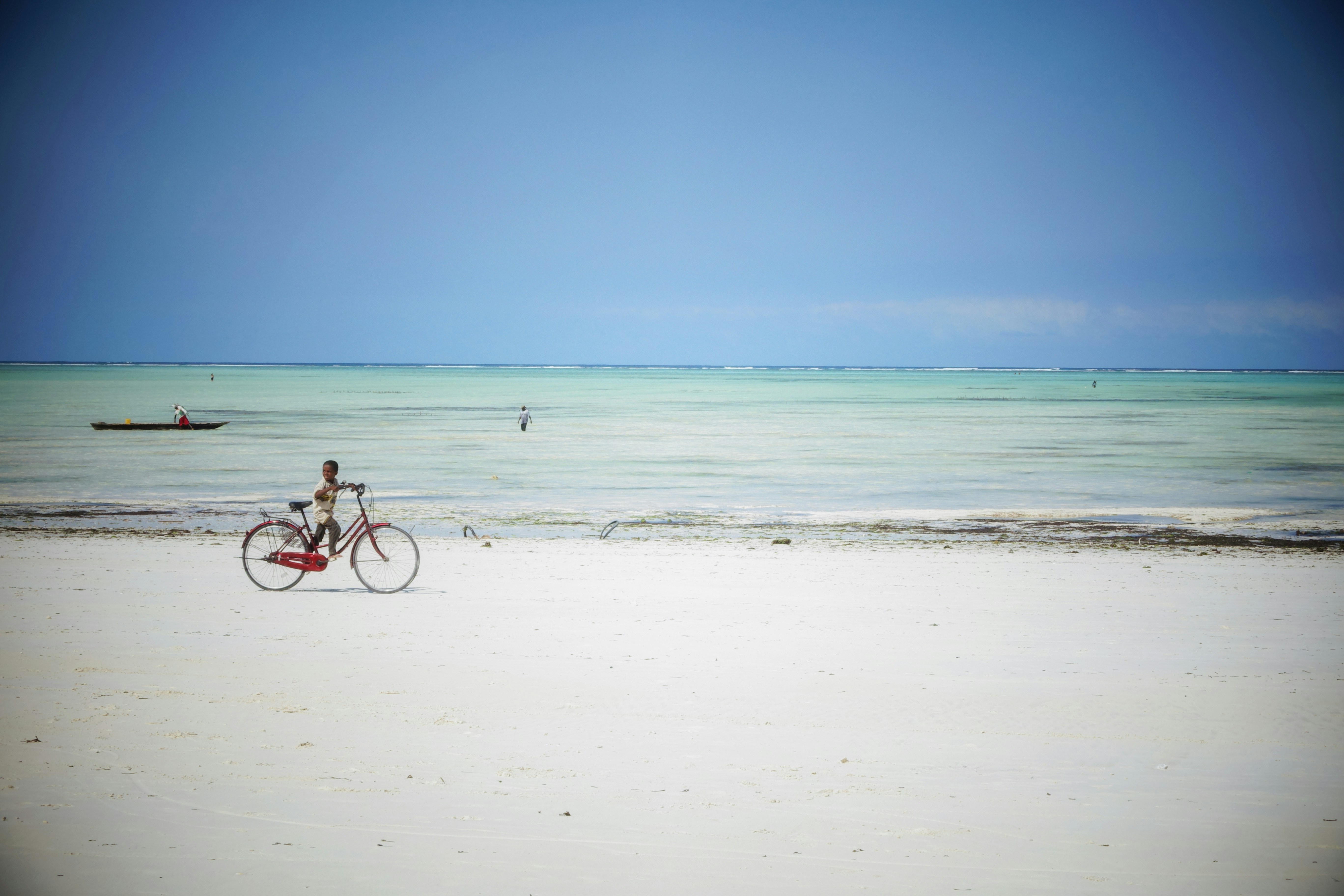 Child riding a bicycle across white sands with the turquoise sea in the background.