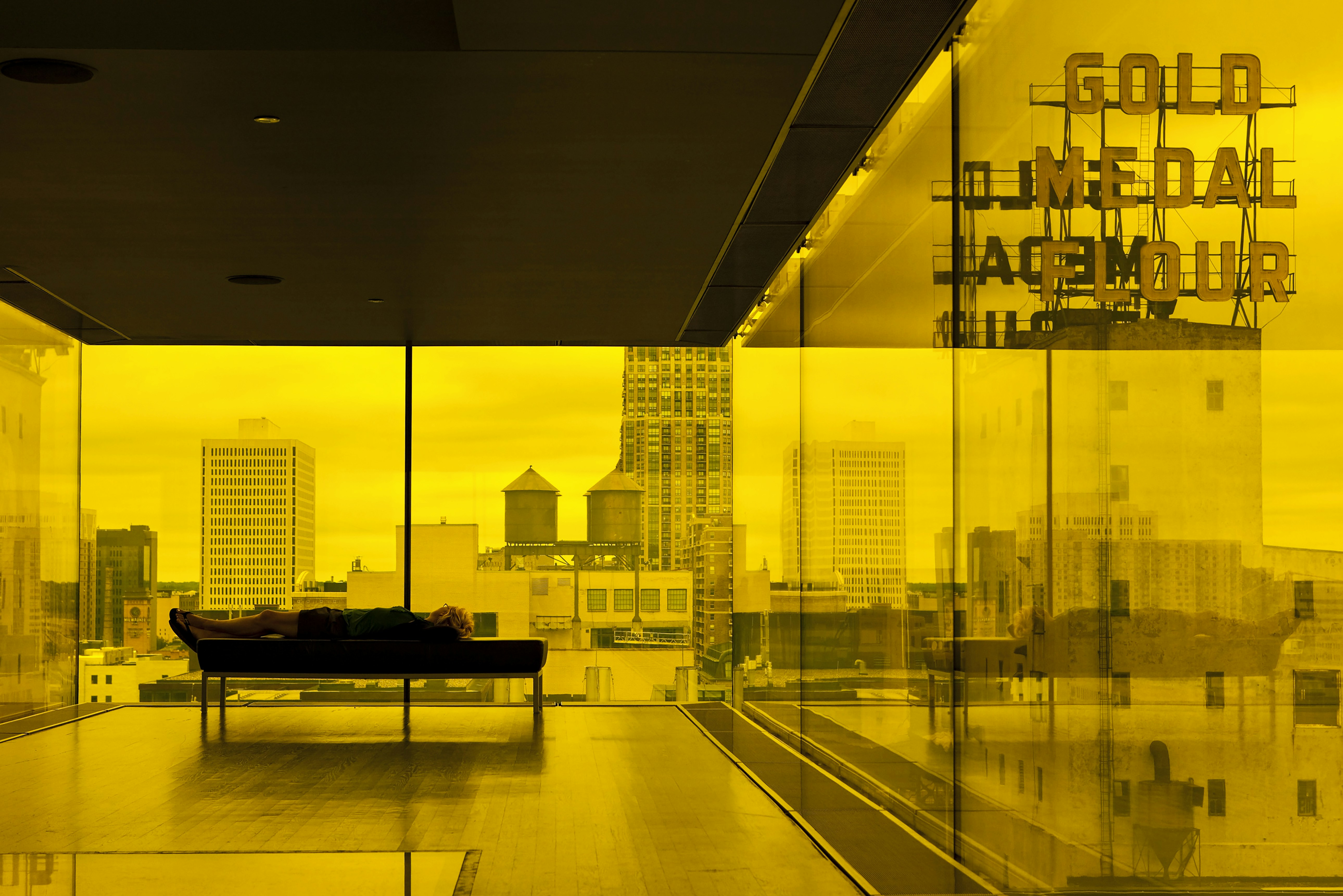 City skyline viewed through yellow-tinted glass with a black sofa silhouetted in the foreground.