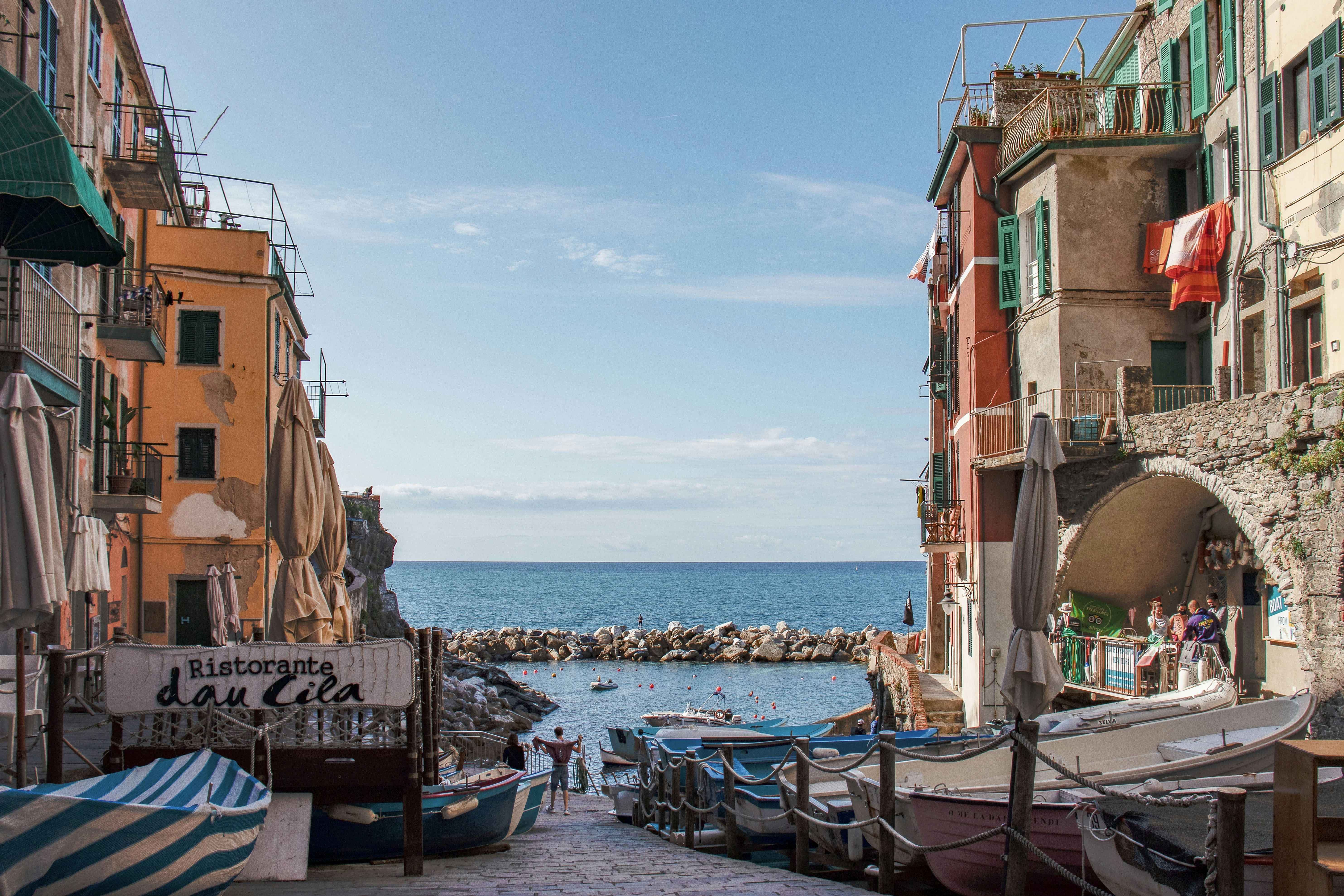 Colorful buildings flank a narrow path leading to a calm harbor in Riomaggiore, Italy.
