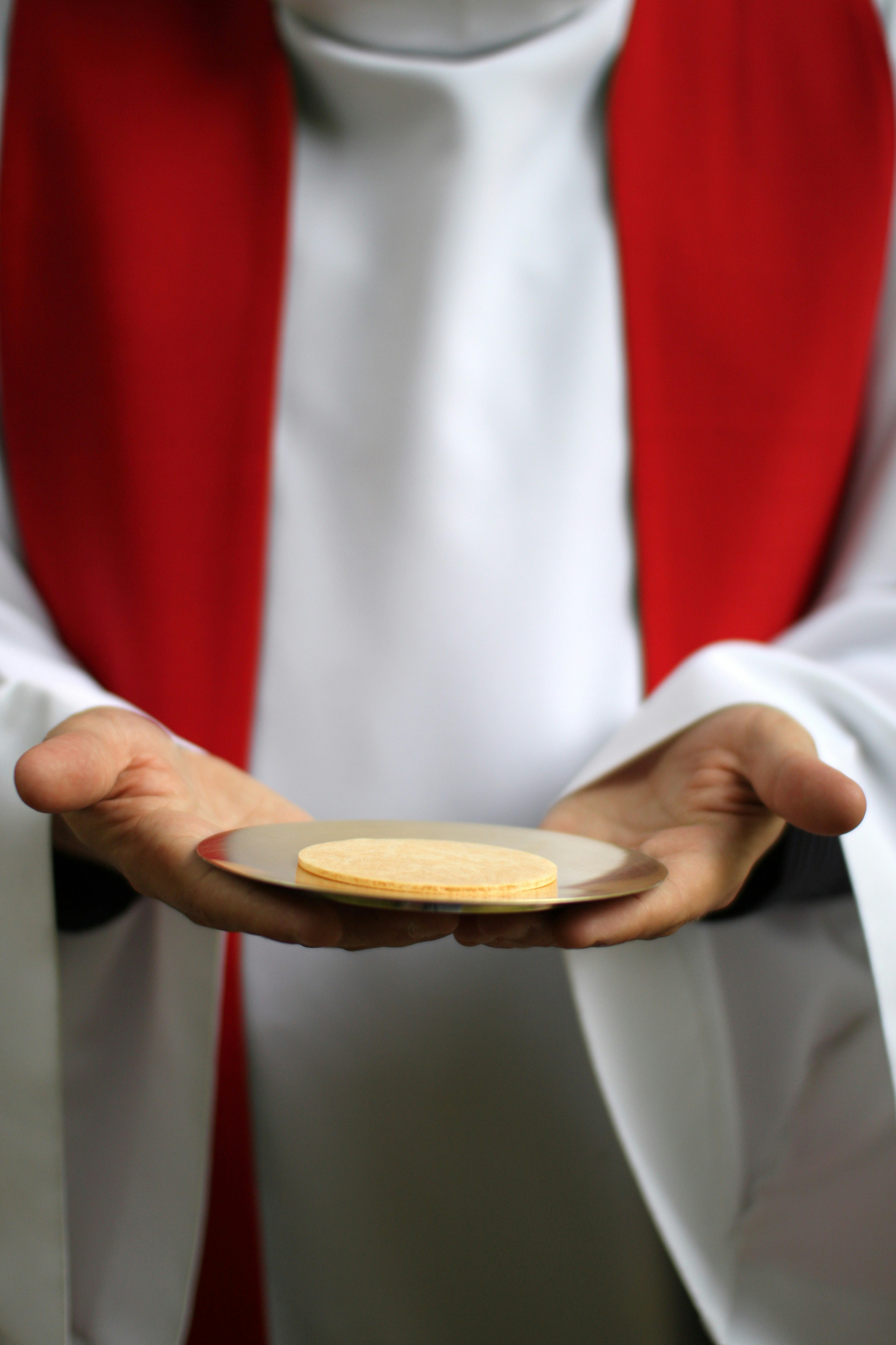 Quiet Communion: A Wafer Presented in Gentle Focus Between White Robes and Red Stole