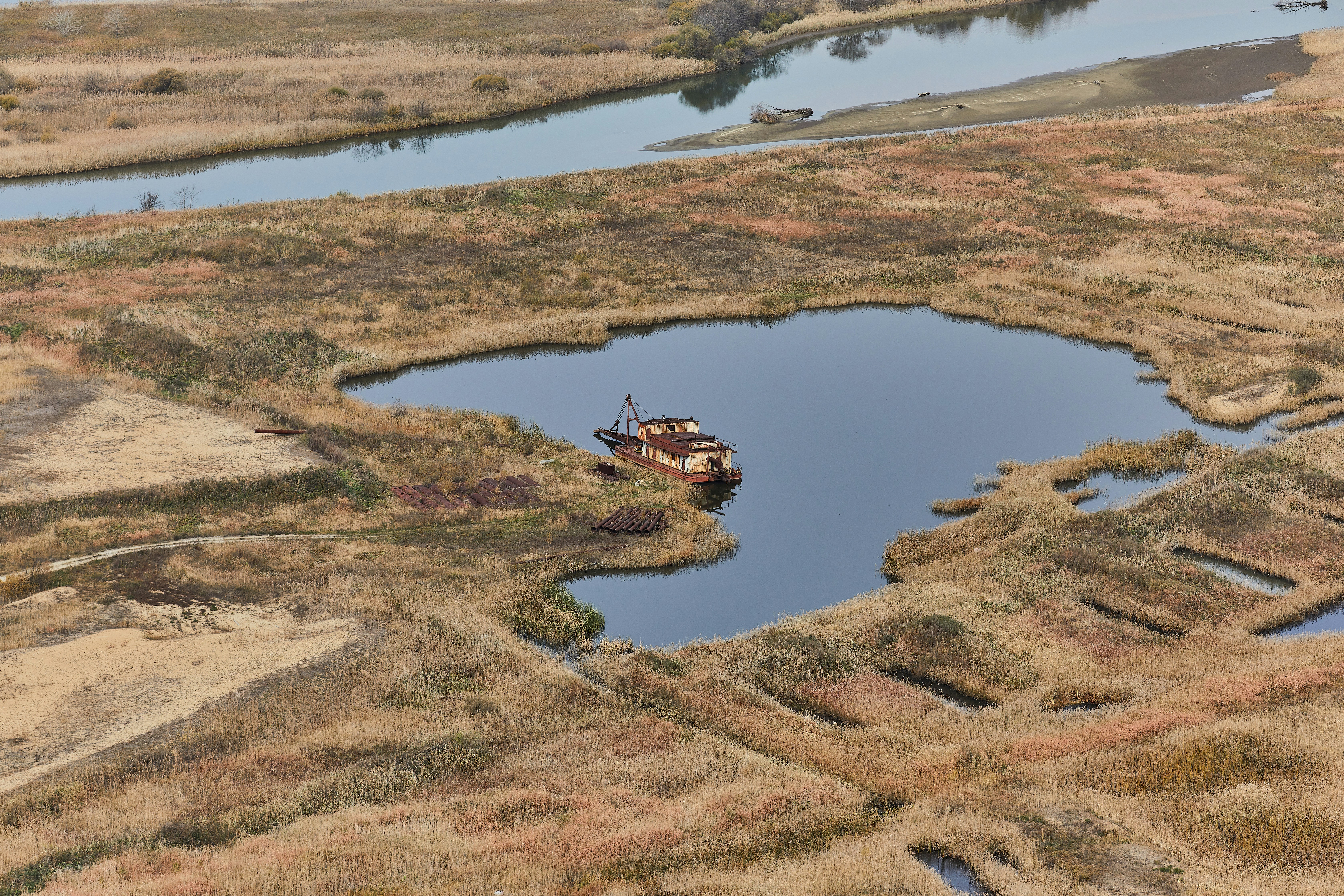 Abandoned boat resting on tranquil waters surrounded by golden marshlands and winding waterways.