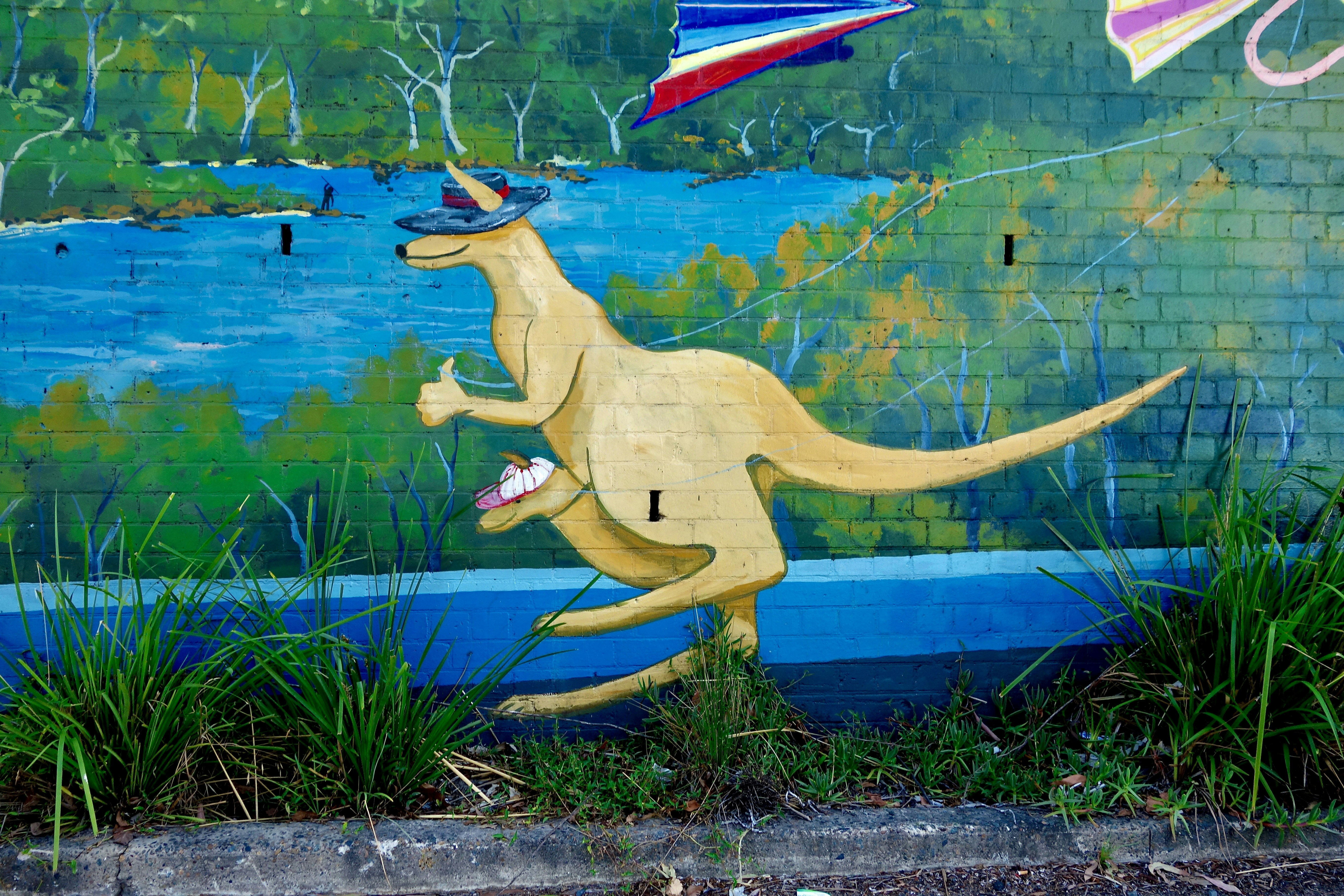 Sunlit Jurassic Graffiti: A Leaning Dino on a Painted Riverbank