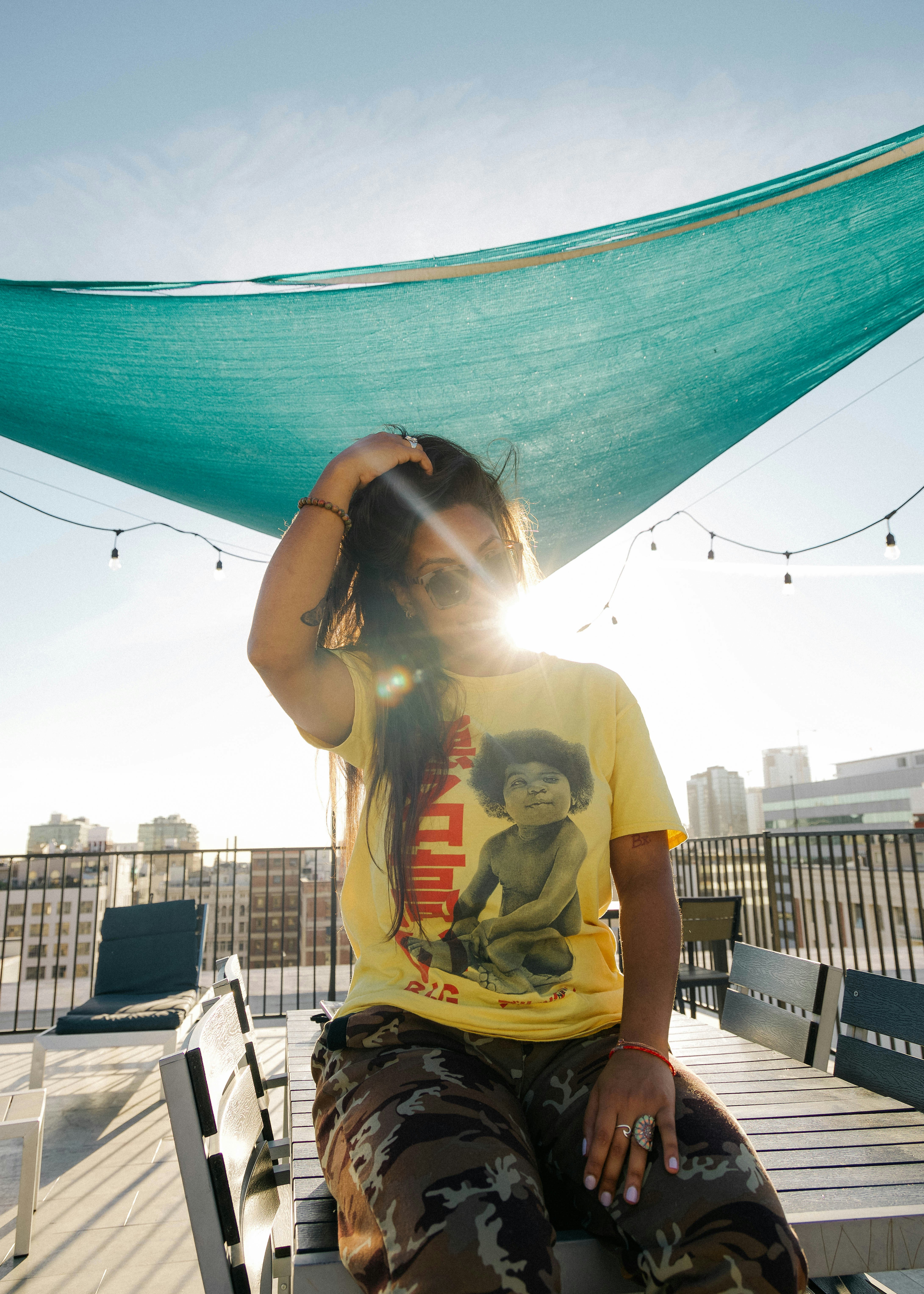 Sunlit Moment on a Rooftop: A Woman in a Yellow Tee Beneath a Turquoise Shade