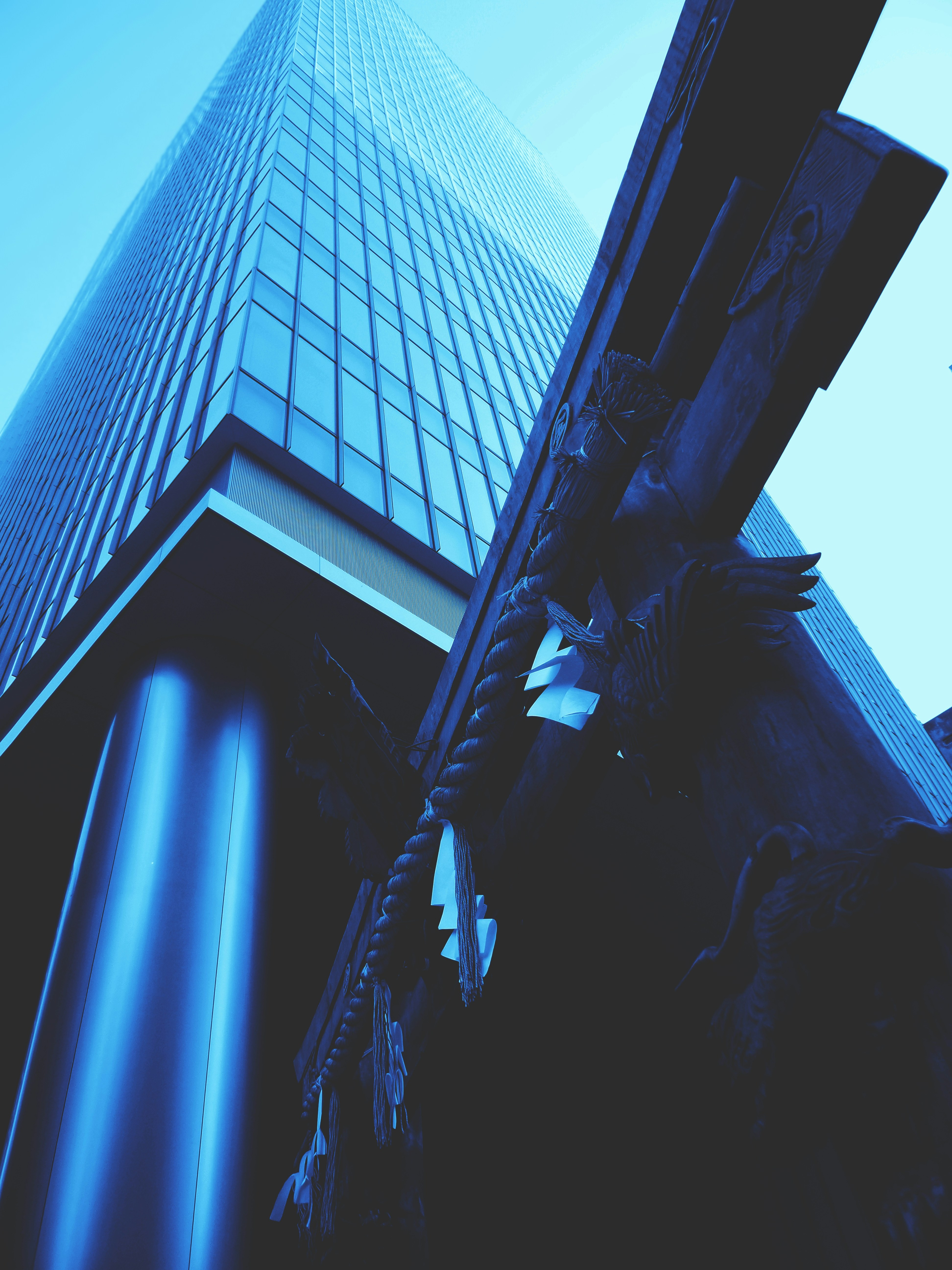 Azure Ascent: Tilted Glass Tower Framing a Shadowed Foreground