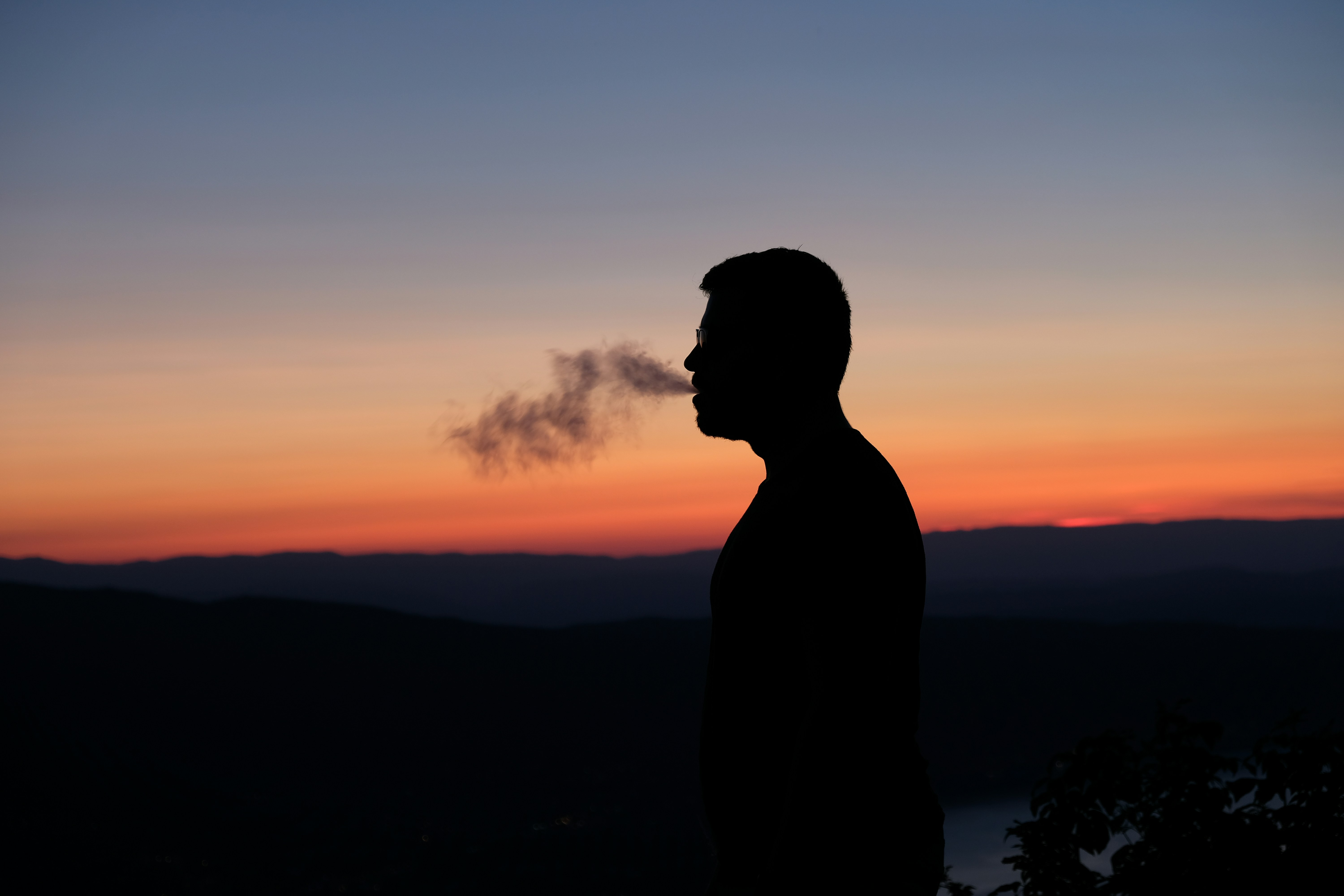 Profile in the Dusk: A lone figure exhales against a velvet sunset.