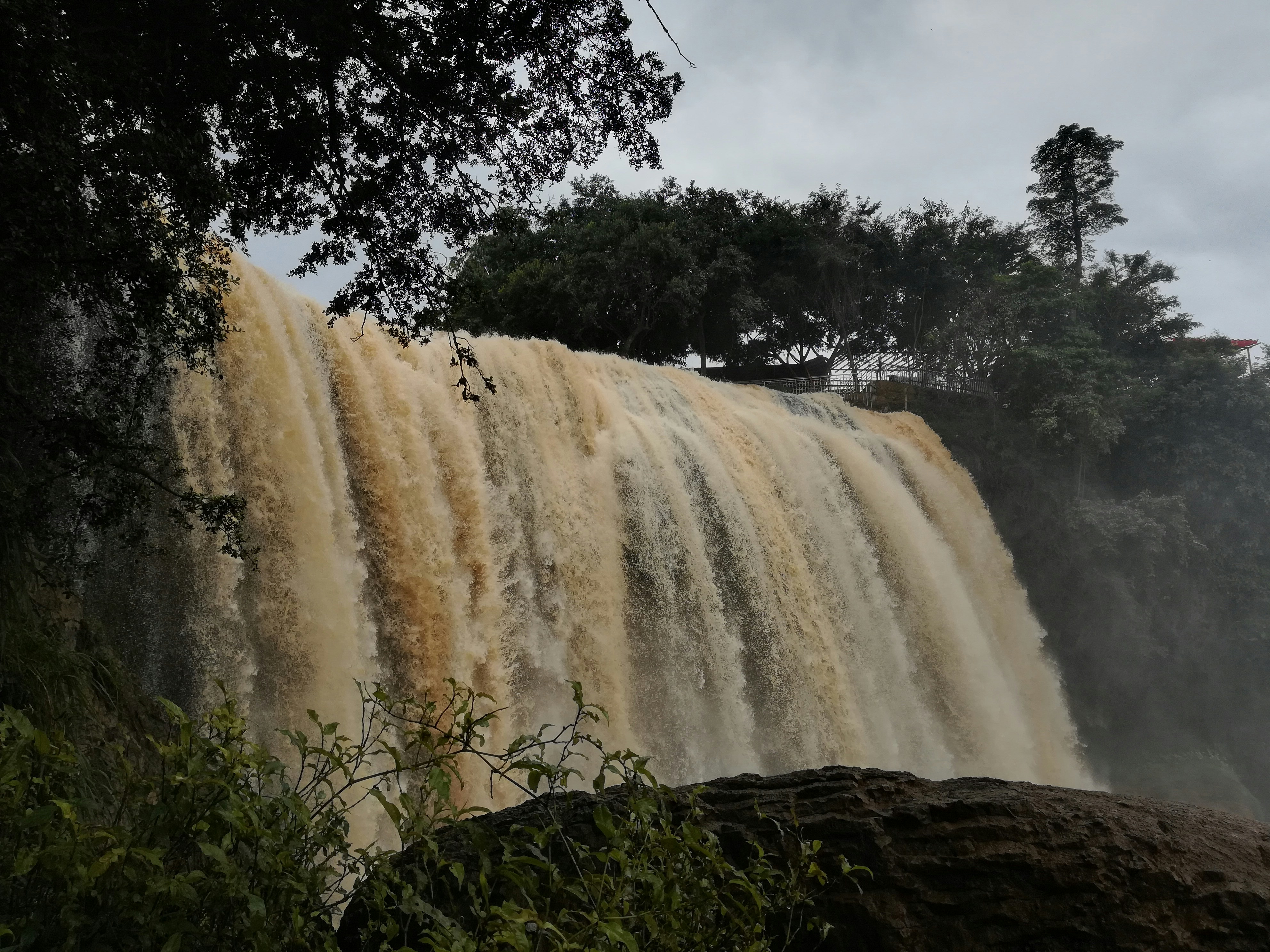 Majestic waterfall plunging over rocky cliffs surrounded by lush greenery under an overcast sky.