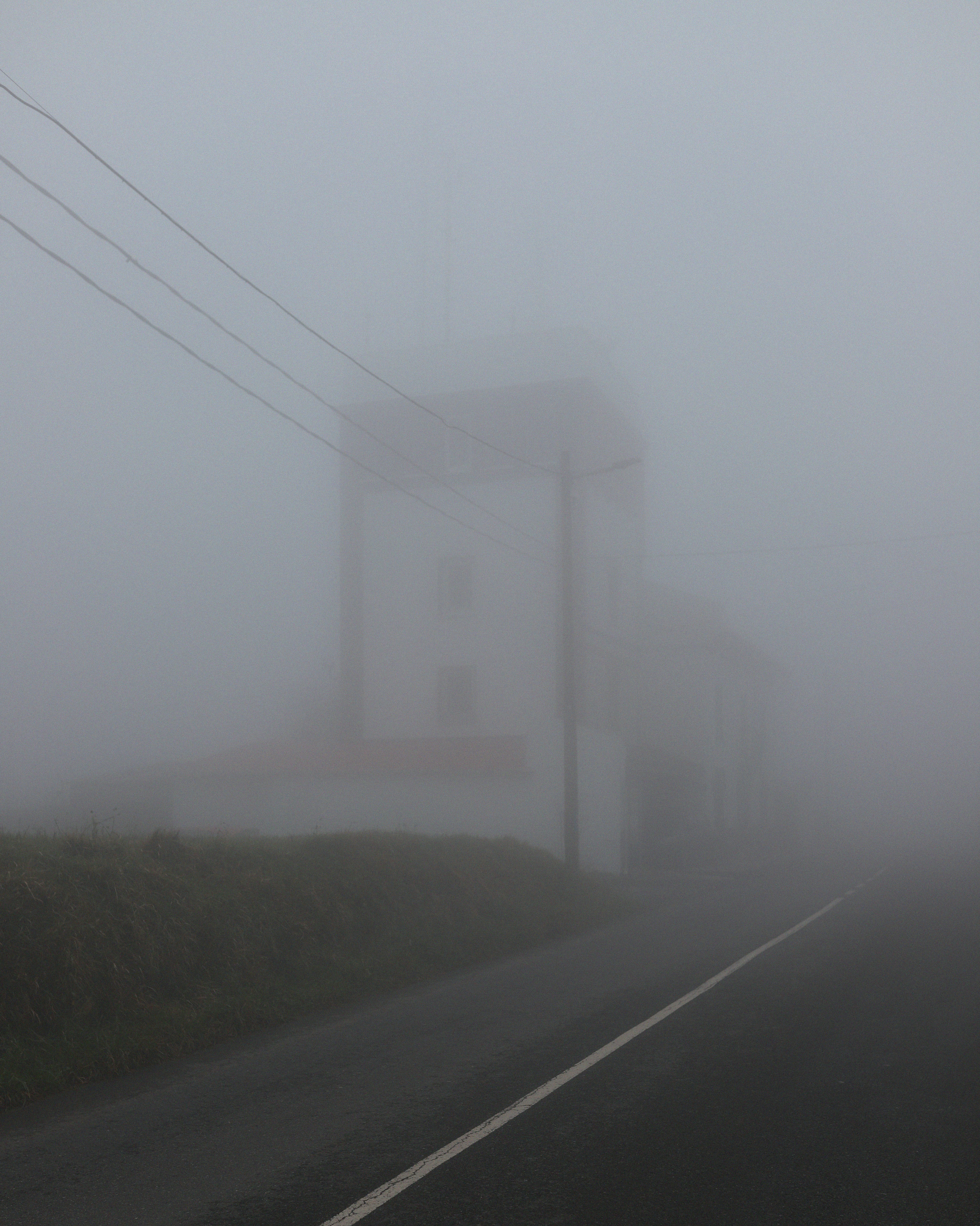 Veiled Approach: Fog Rolls Across the Road Toward a Distant Building