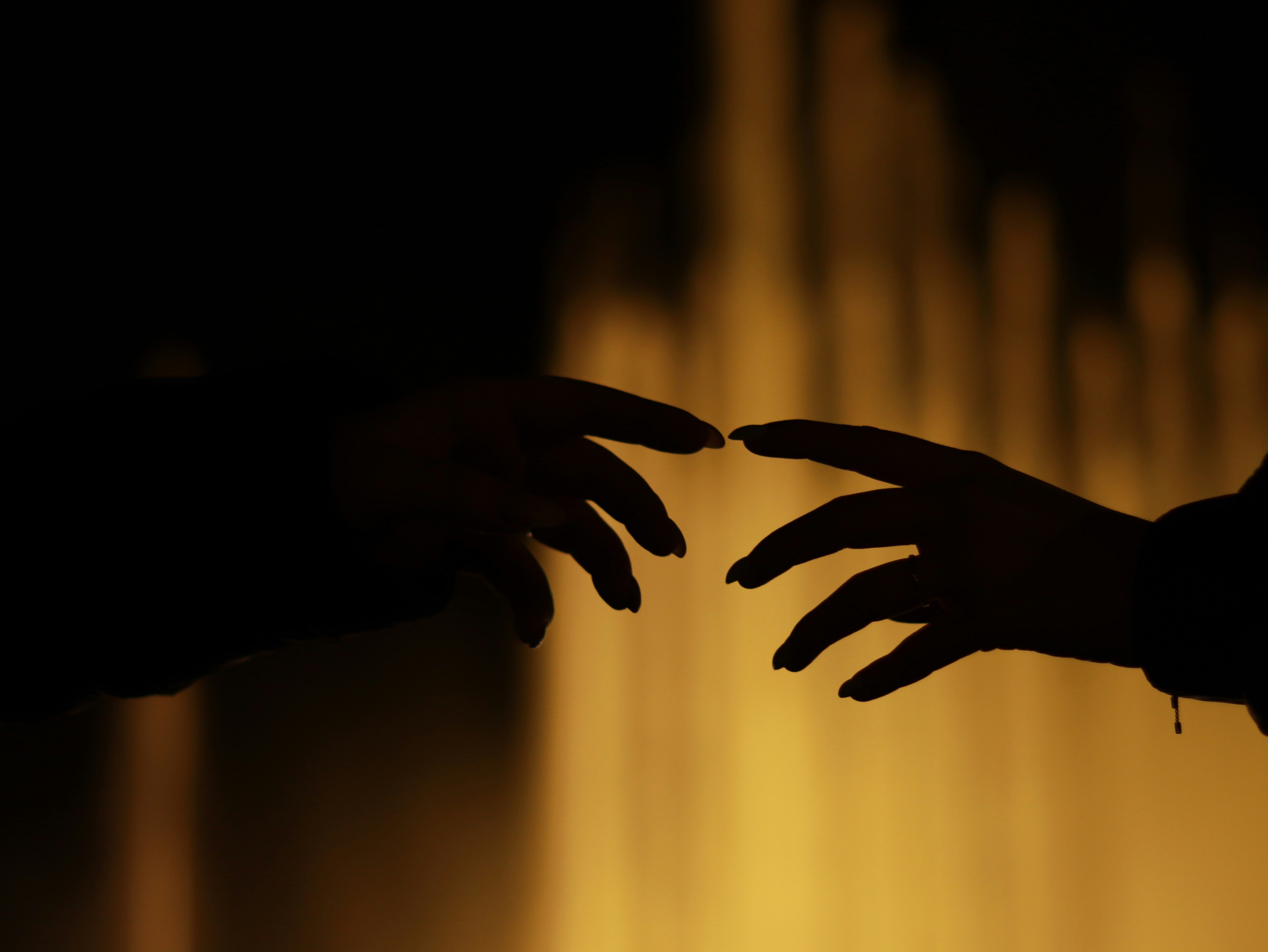 Two hands reaching out to each other against a backdrop of illuminated water, creating a striking silhouette effect.
