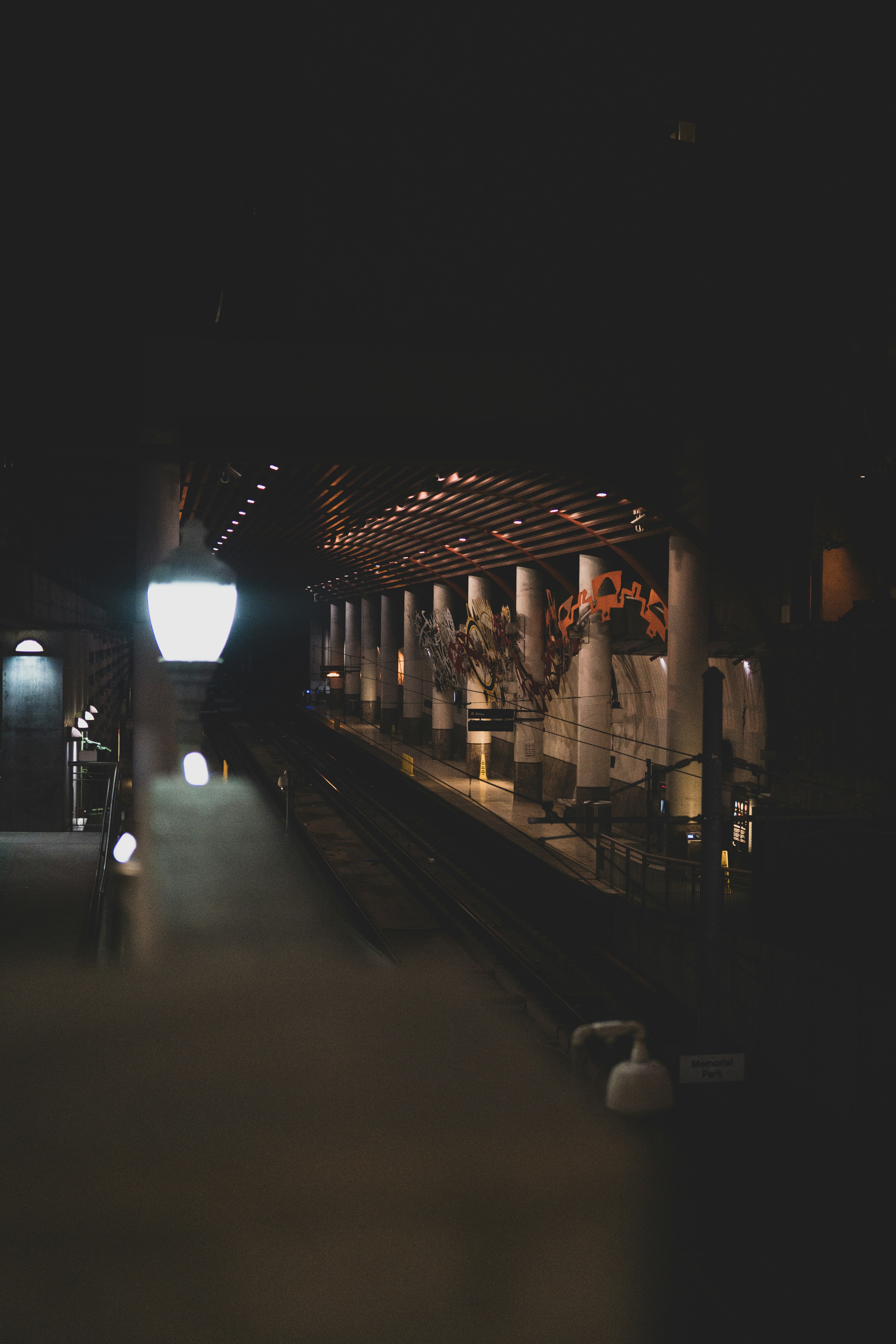 Illuminated train station platform with artistic murals and glowing street lamps under a dark sky.
