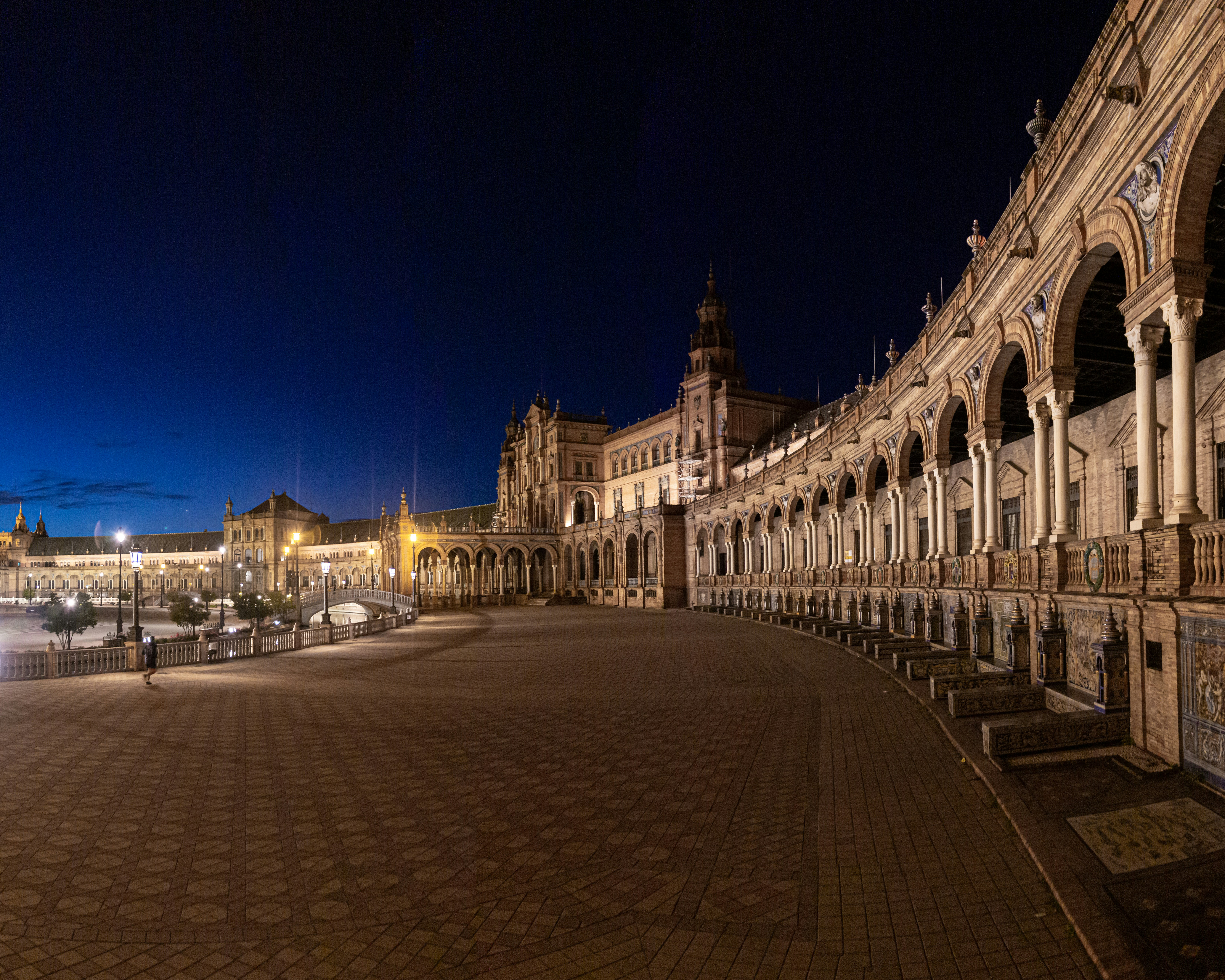 Curved colonnade of Plaza de España illuminated against a deep blue twilight sky.