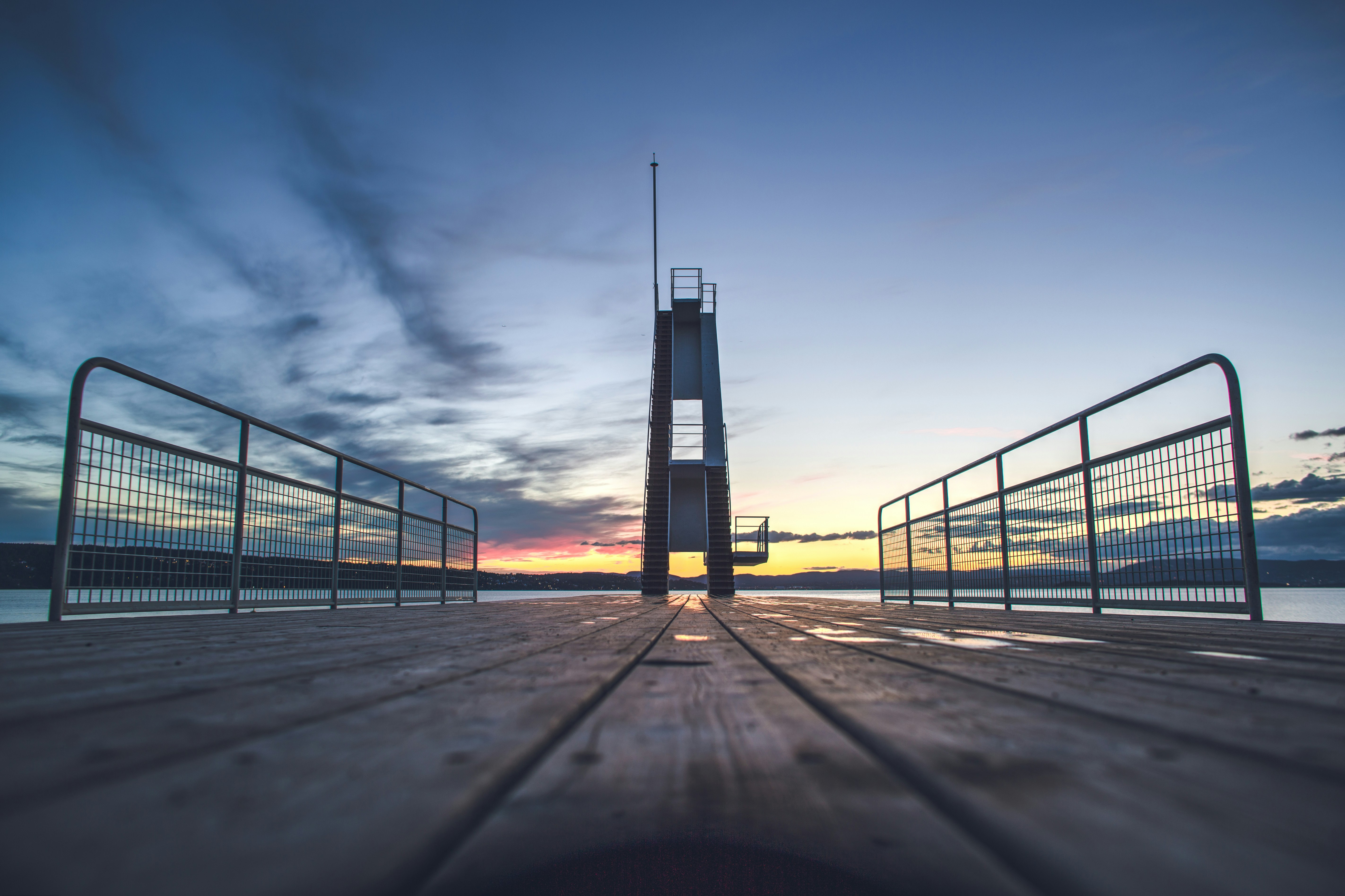 Wooden pier leading to a diving board silhouetted against a vibrant sunset sky.