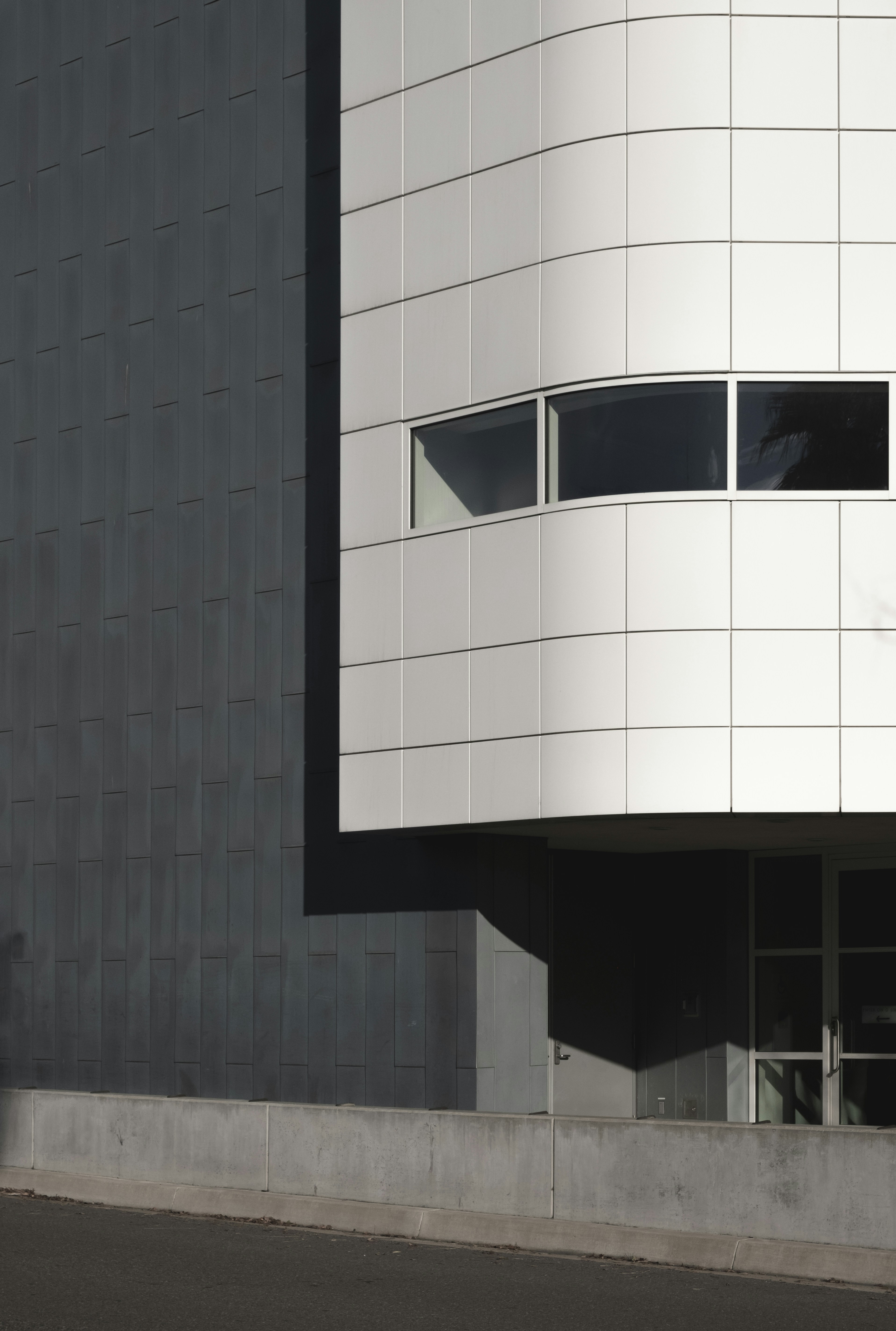 Sleek, curved white facade of a modern building contrasted against a textured dark wall, showcasing geometric design elements.