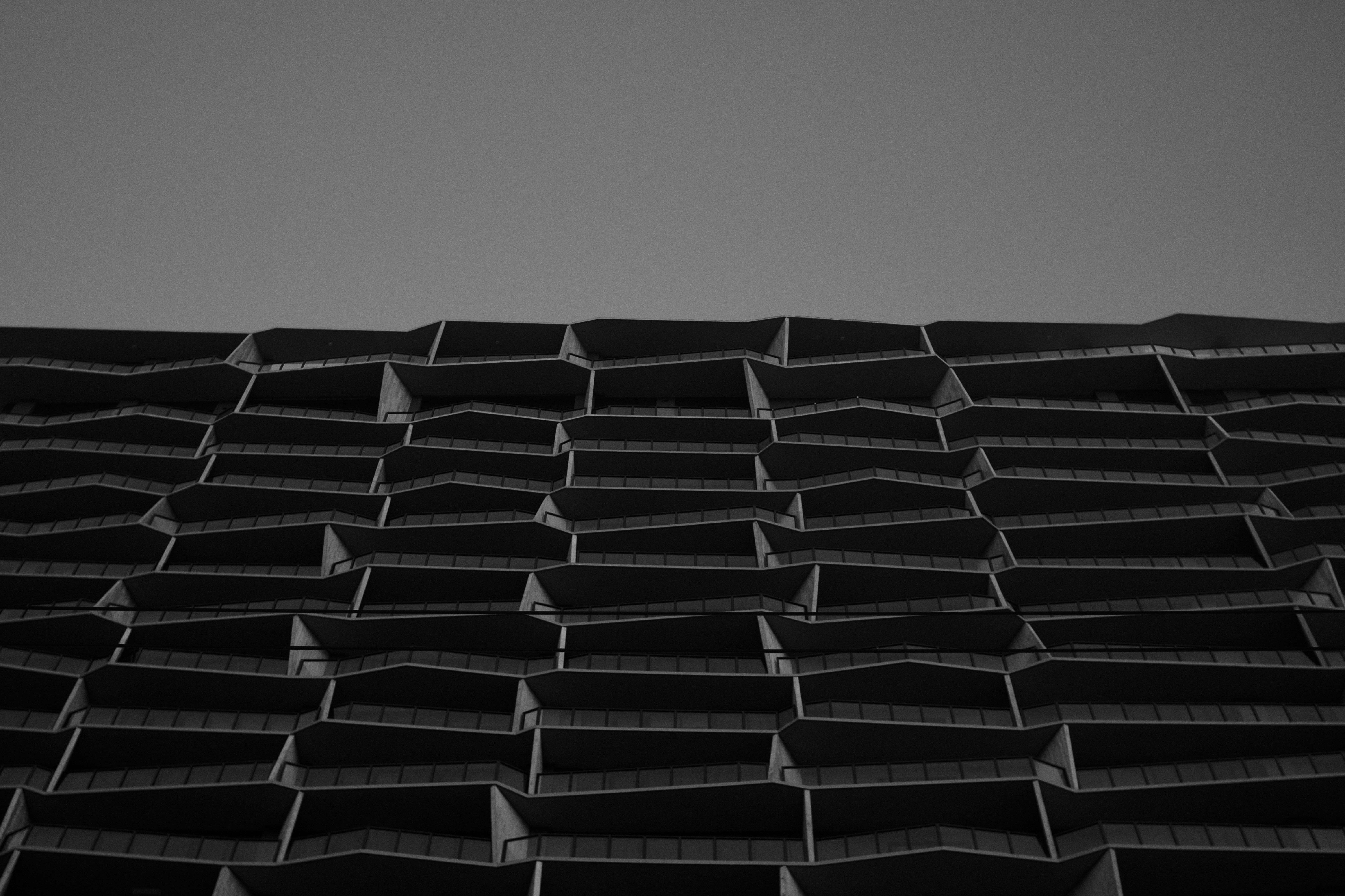 Abstract view of a modern building facade showcasing a wave-like pattern of balconies in monochrome. The design emphasizes geometric forms and contrasts.
