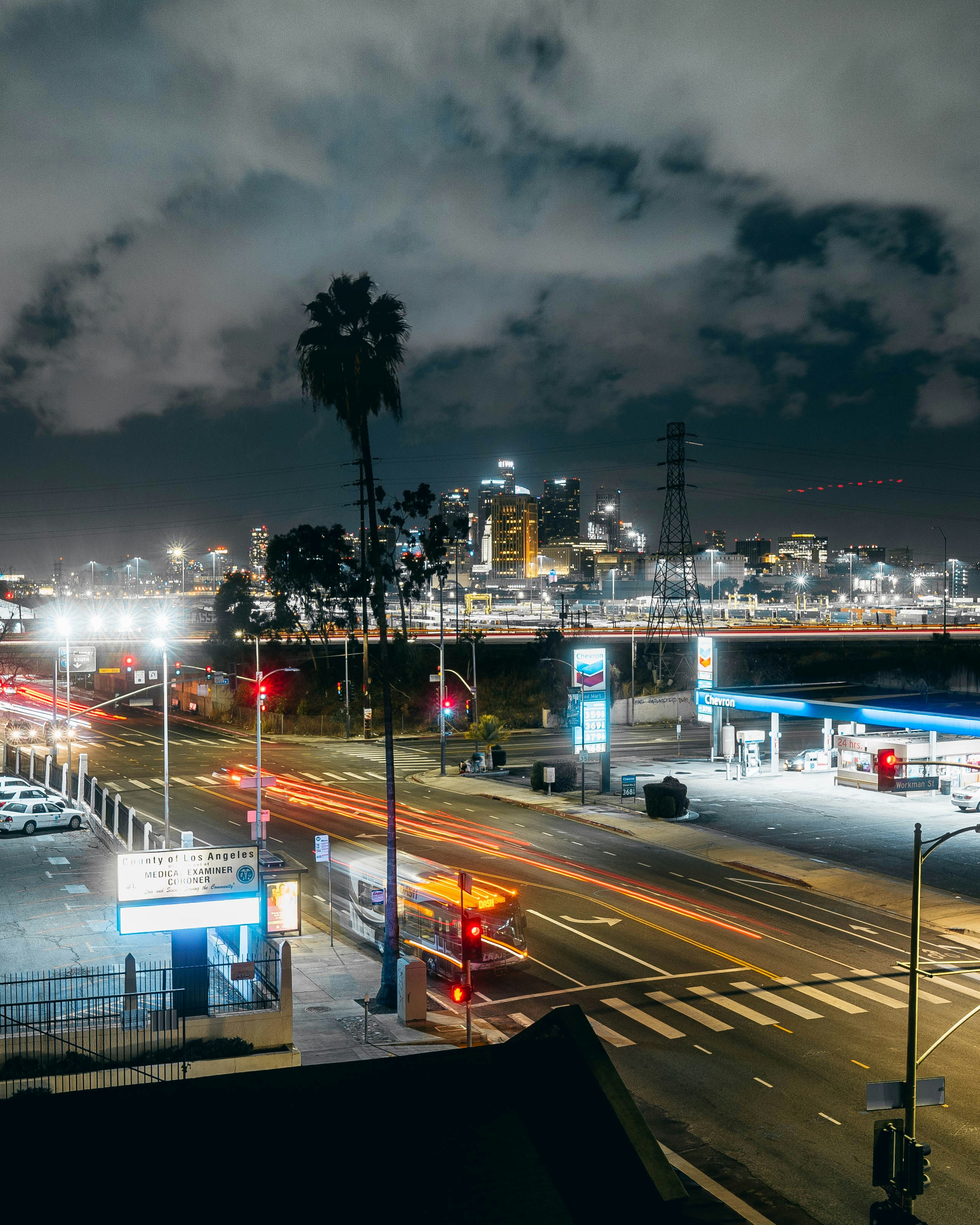 Illuminated city skyline at night, featuring traffic trails and palm trees, showcasing the vibrancy of urban life.