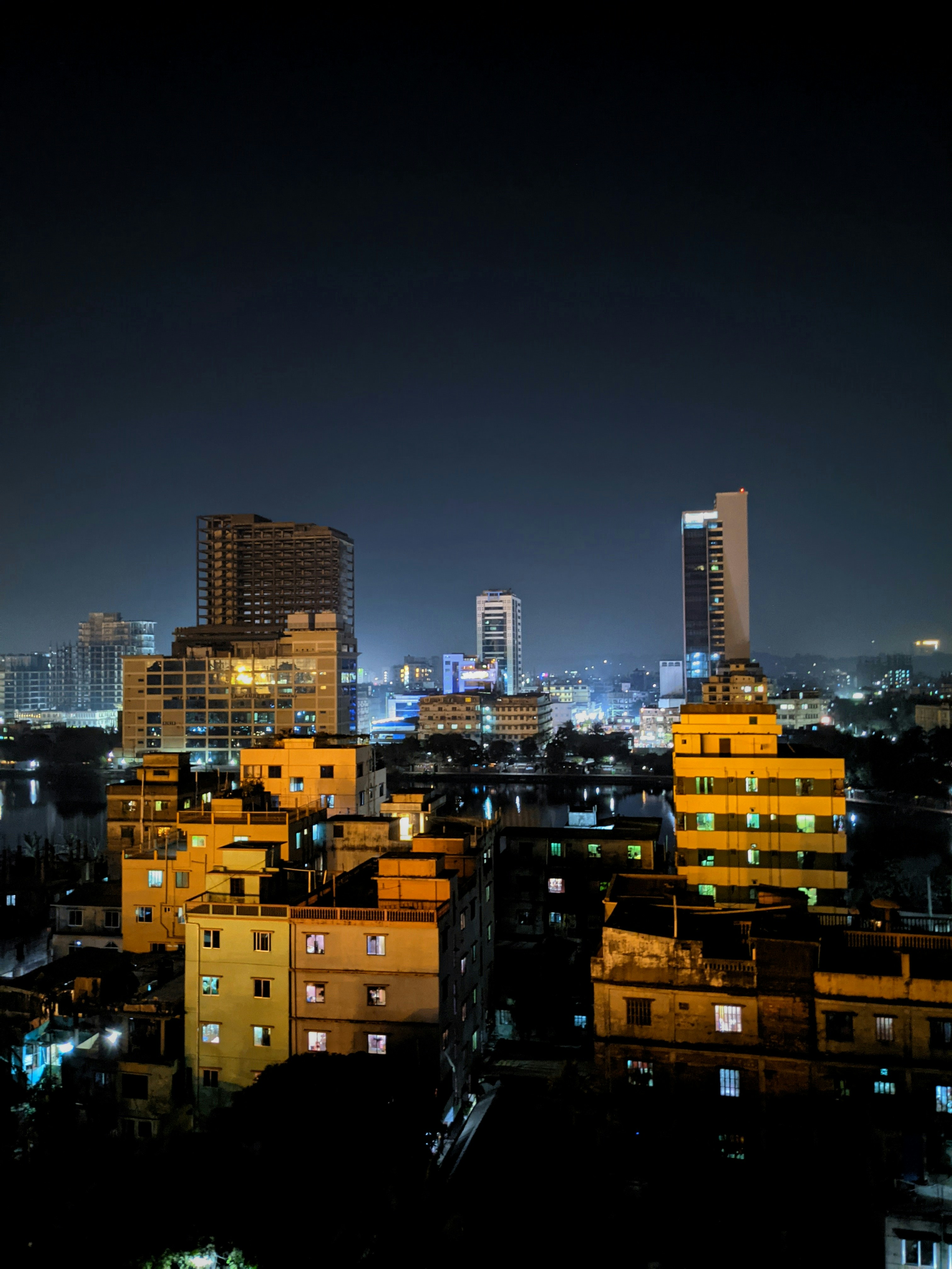 Vibrant cityscape at night showcasing illuminated buildings and residential structures. The scene captures the pulse of urban life under a dark sky.
