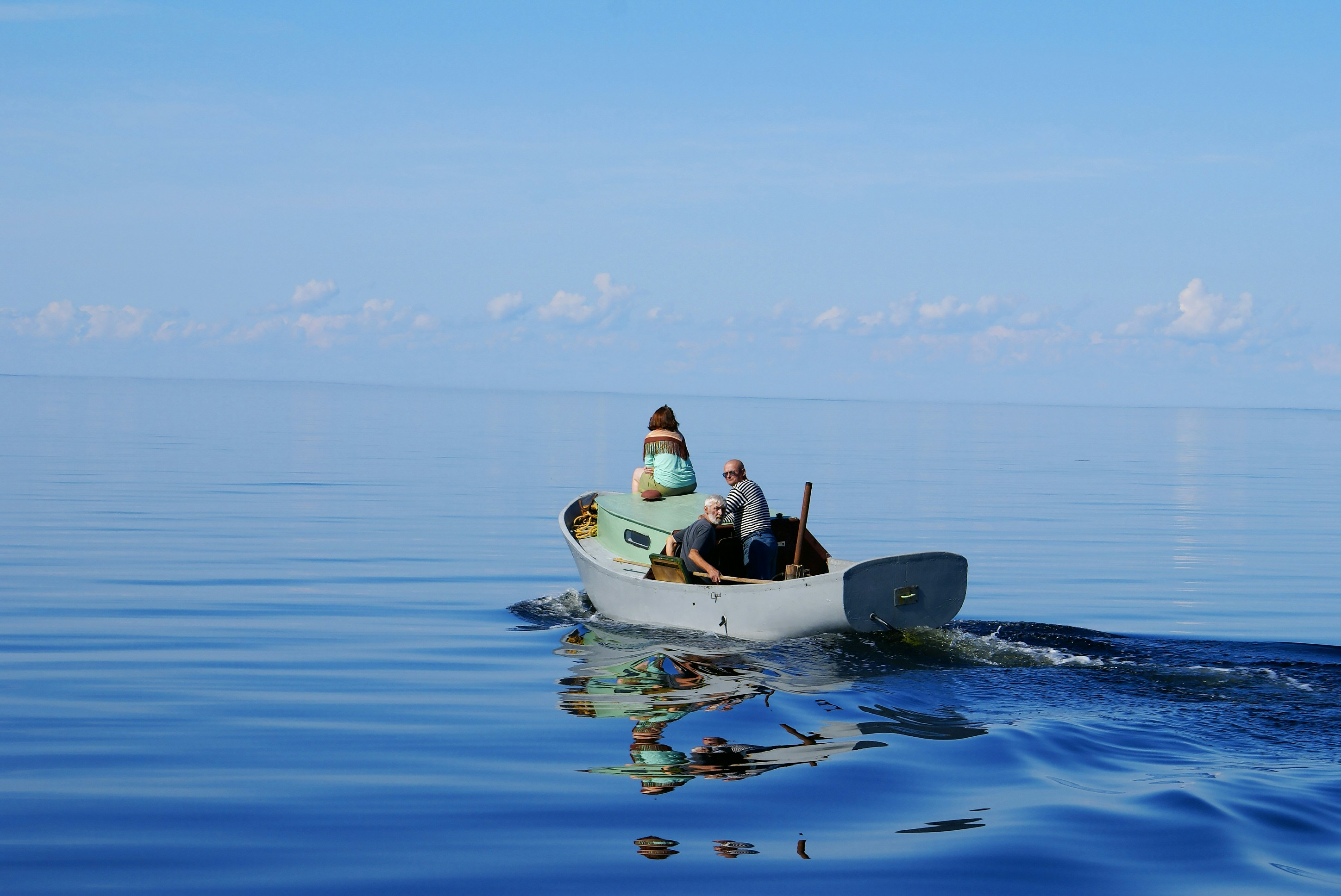 Two people in a small boat navigating calm blue waters under a clear sky.