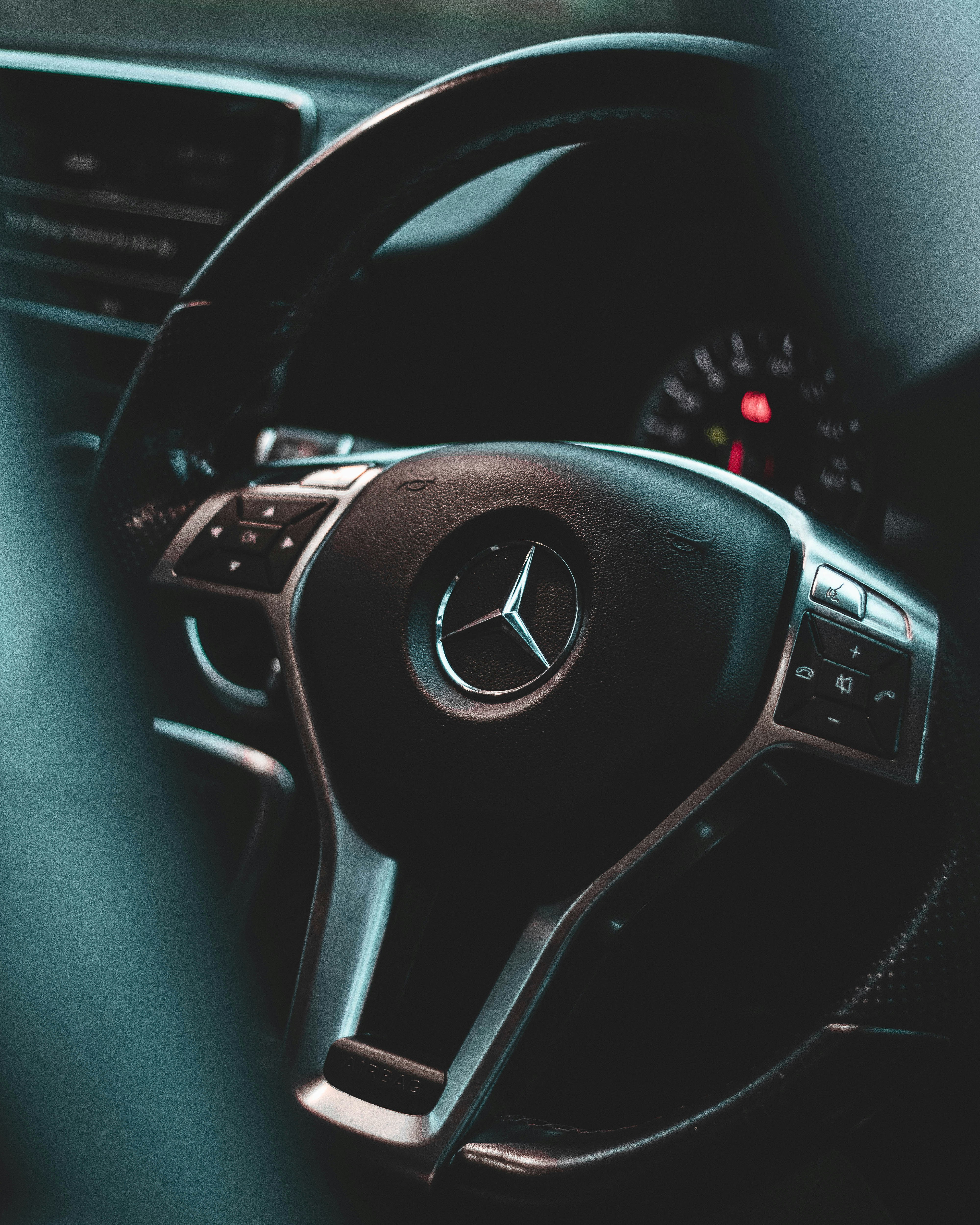 Close-up of a Mercedes-Benz steering wheel showcasing its sleek design and high-quality materials. The dashboard elements blur in the background, emphasizing the luxurious interior.