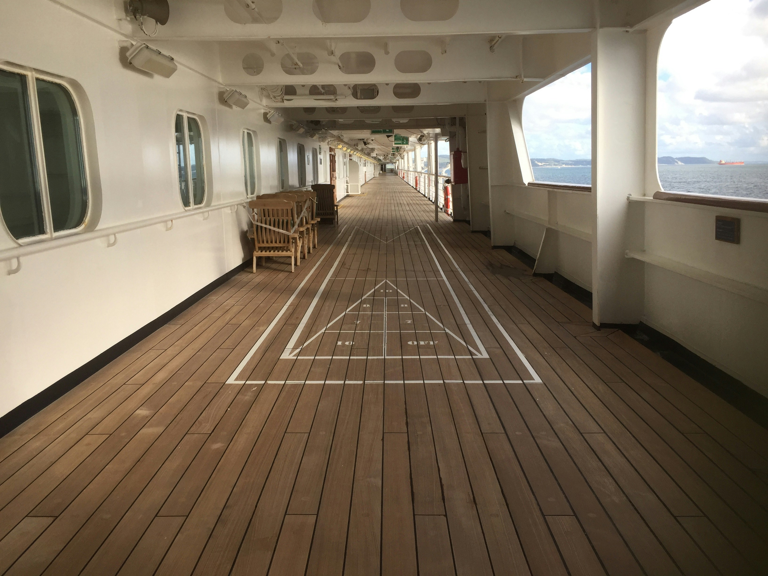 Wooden deck of a ship featuring a triangular pattern and empty benches, with expansive ocean views beyond the railings.