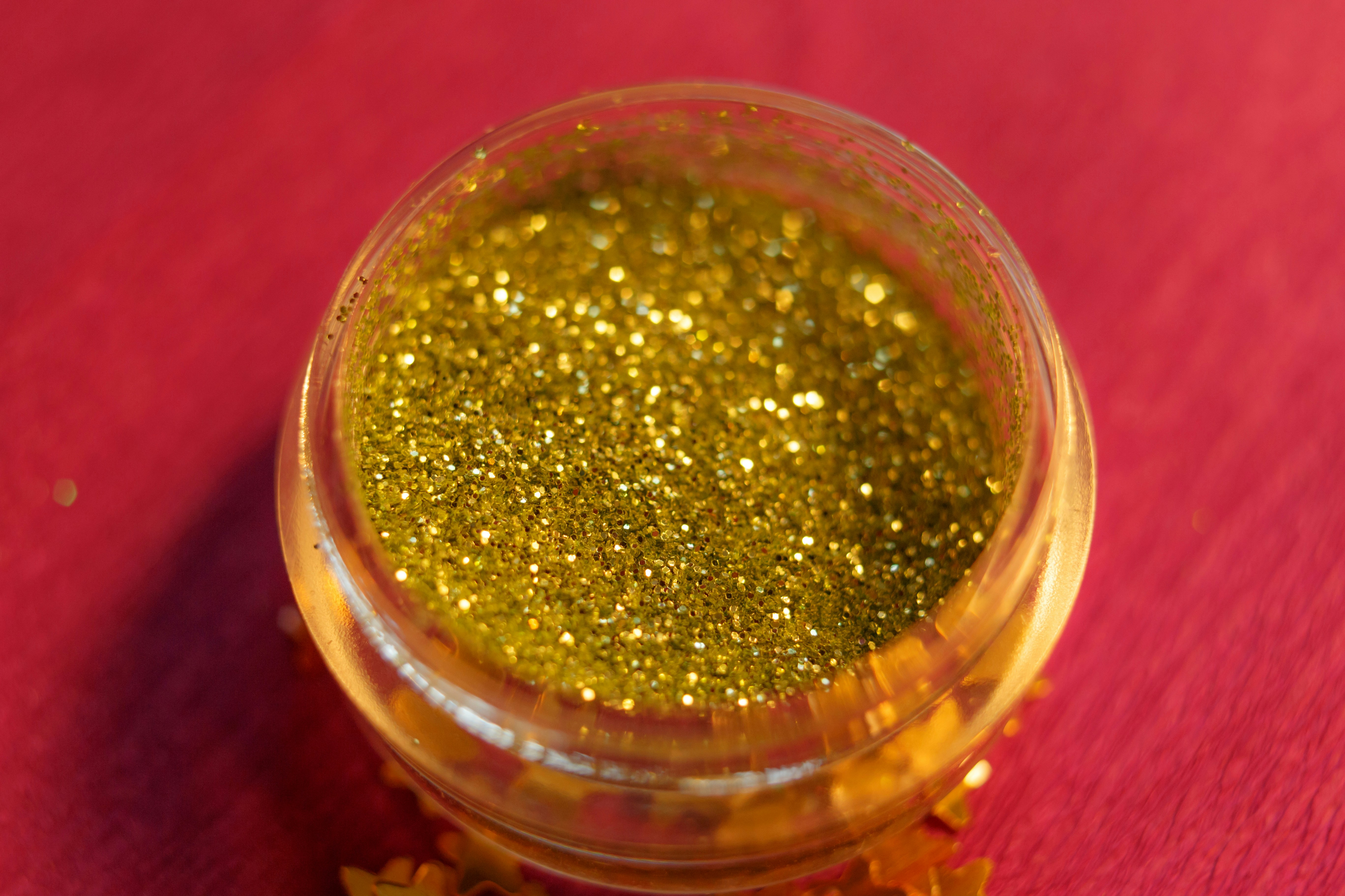Close-up of a jar filled with shimmering golden glitter on a vibrant red surface.