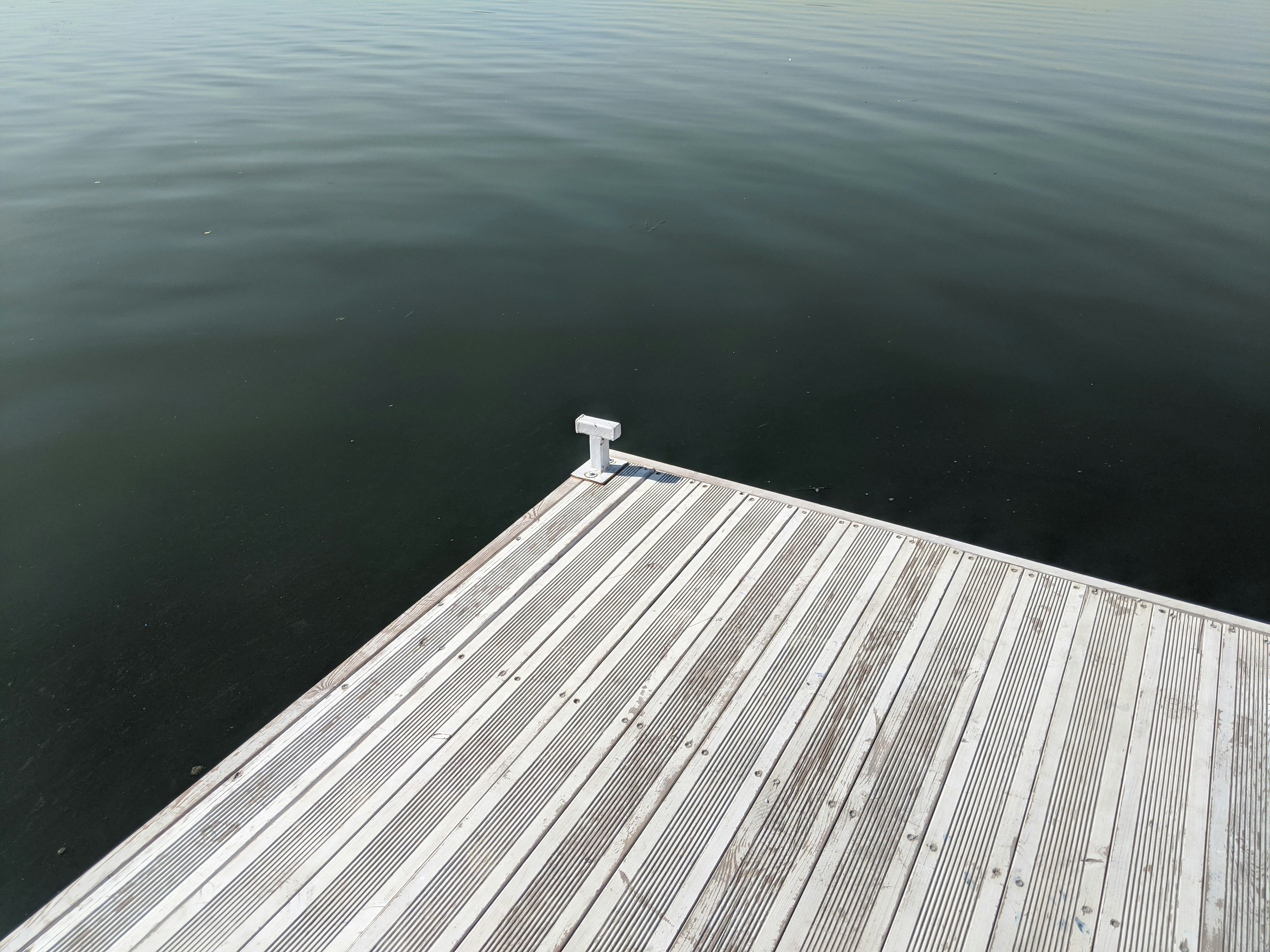 Wooden dock extending into calm water, reflecting soft light. A solitary cleat stands at the edge.