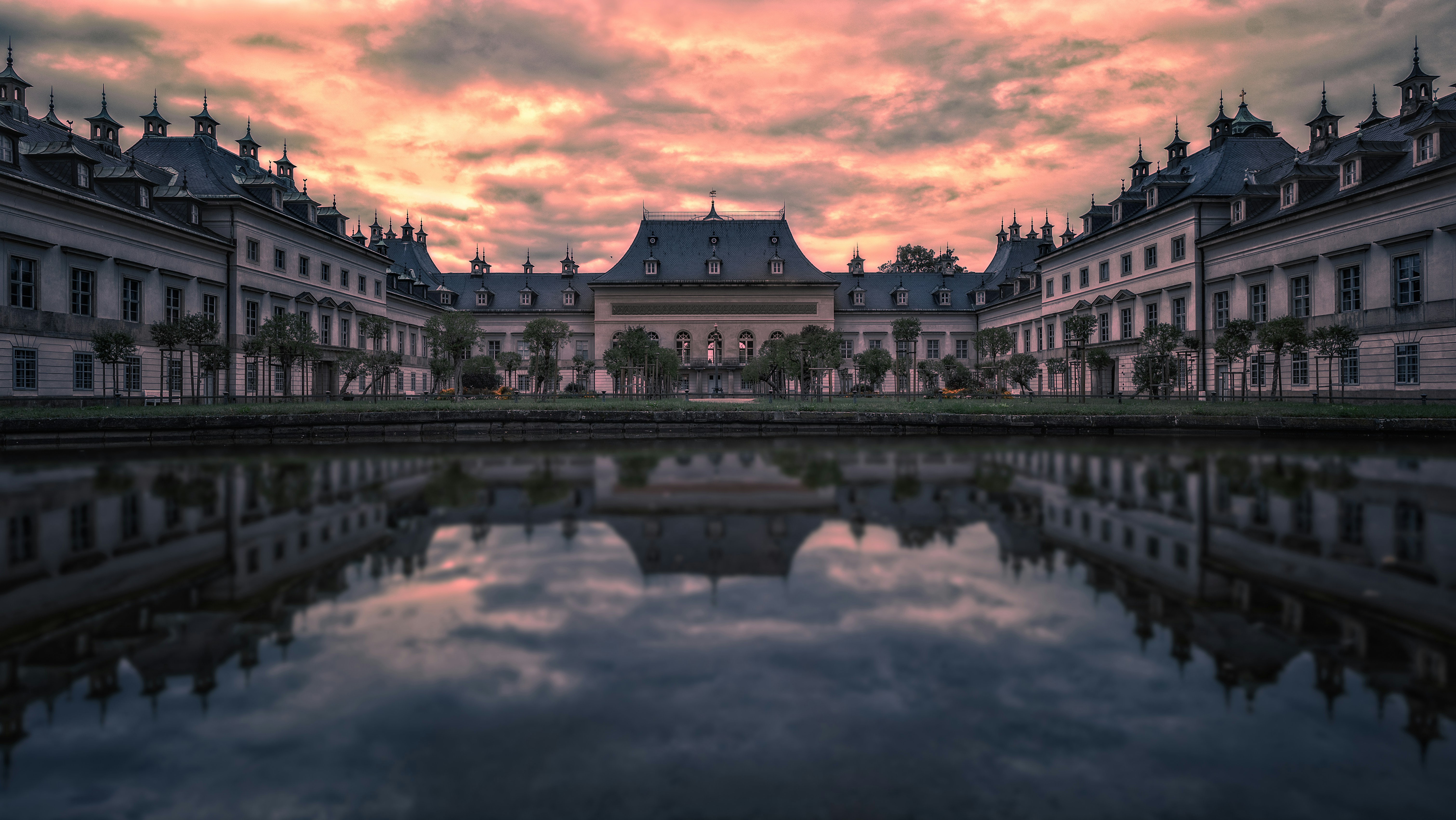 Symmetrical architecture mirrored in a tranquil water body under a dramatic sunset sky.