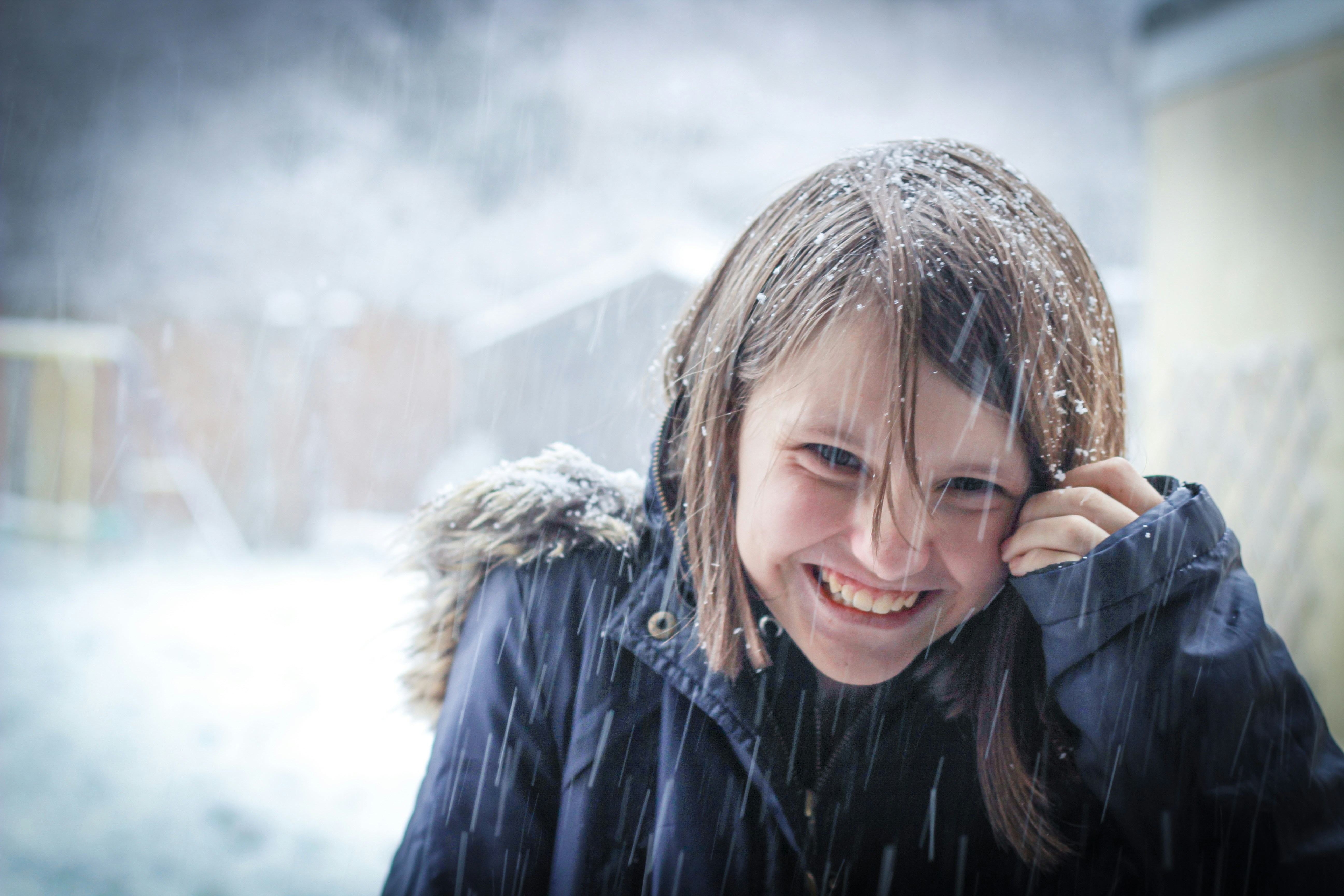 Girl laughing joyfully in a snowstorm, her hair dusted with snowflakes, capturing the essence of winter playfulness.