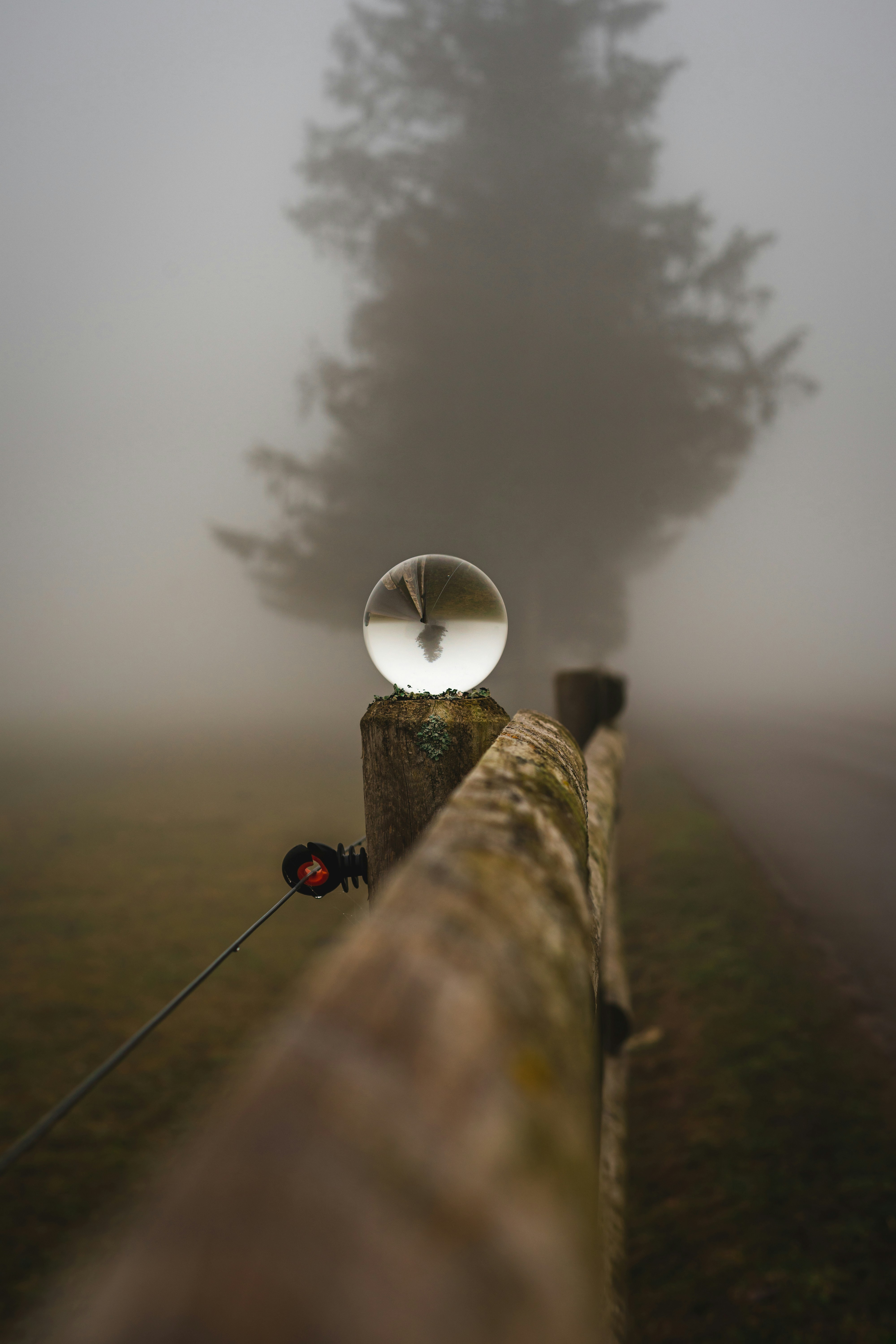 Orb in the Mist: A Glass Sphere Resting on a Weathered Fence Post