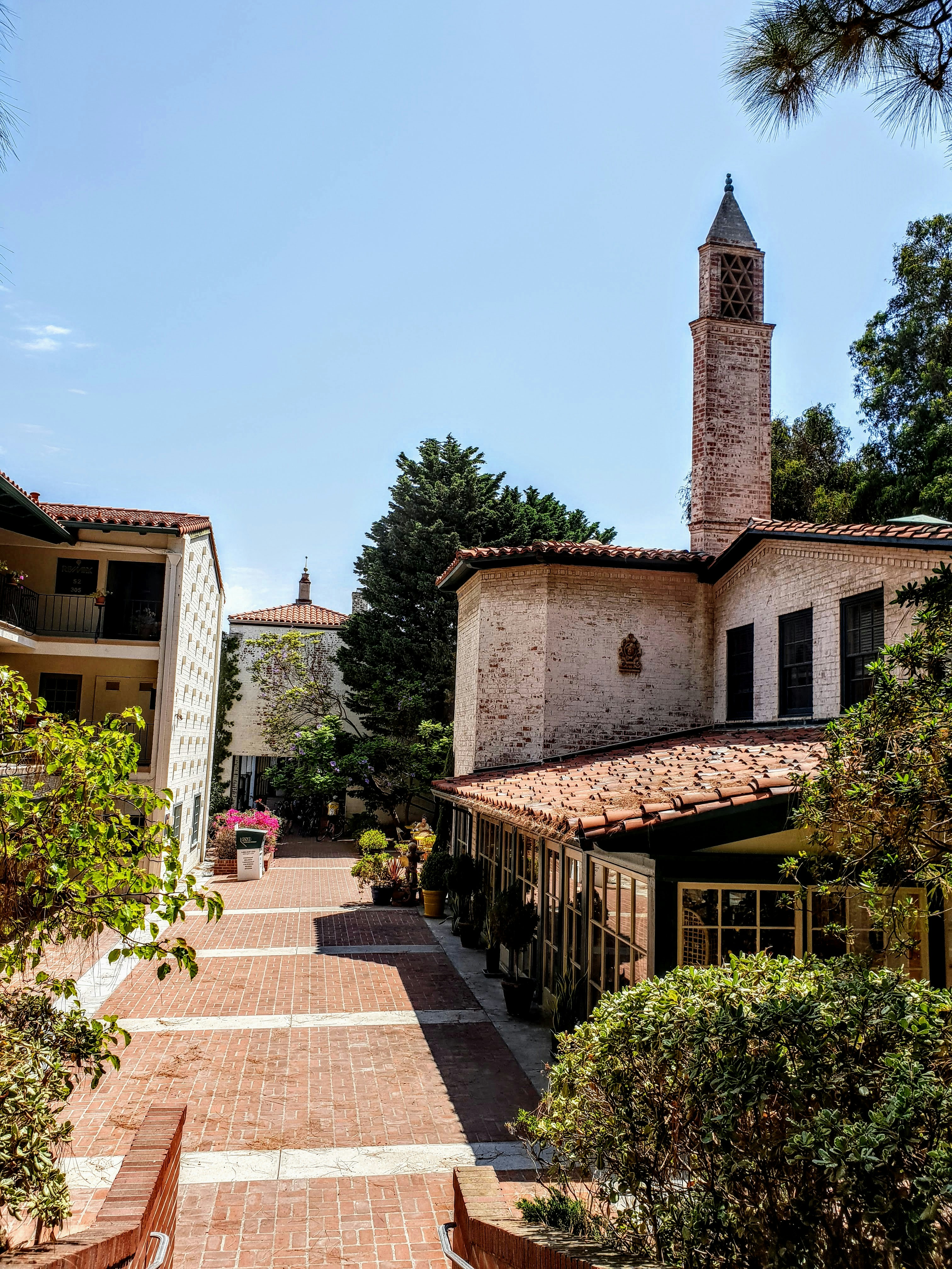 Sunlit courtyard with rustic buildings and lush greenery under a clear blue sky.