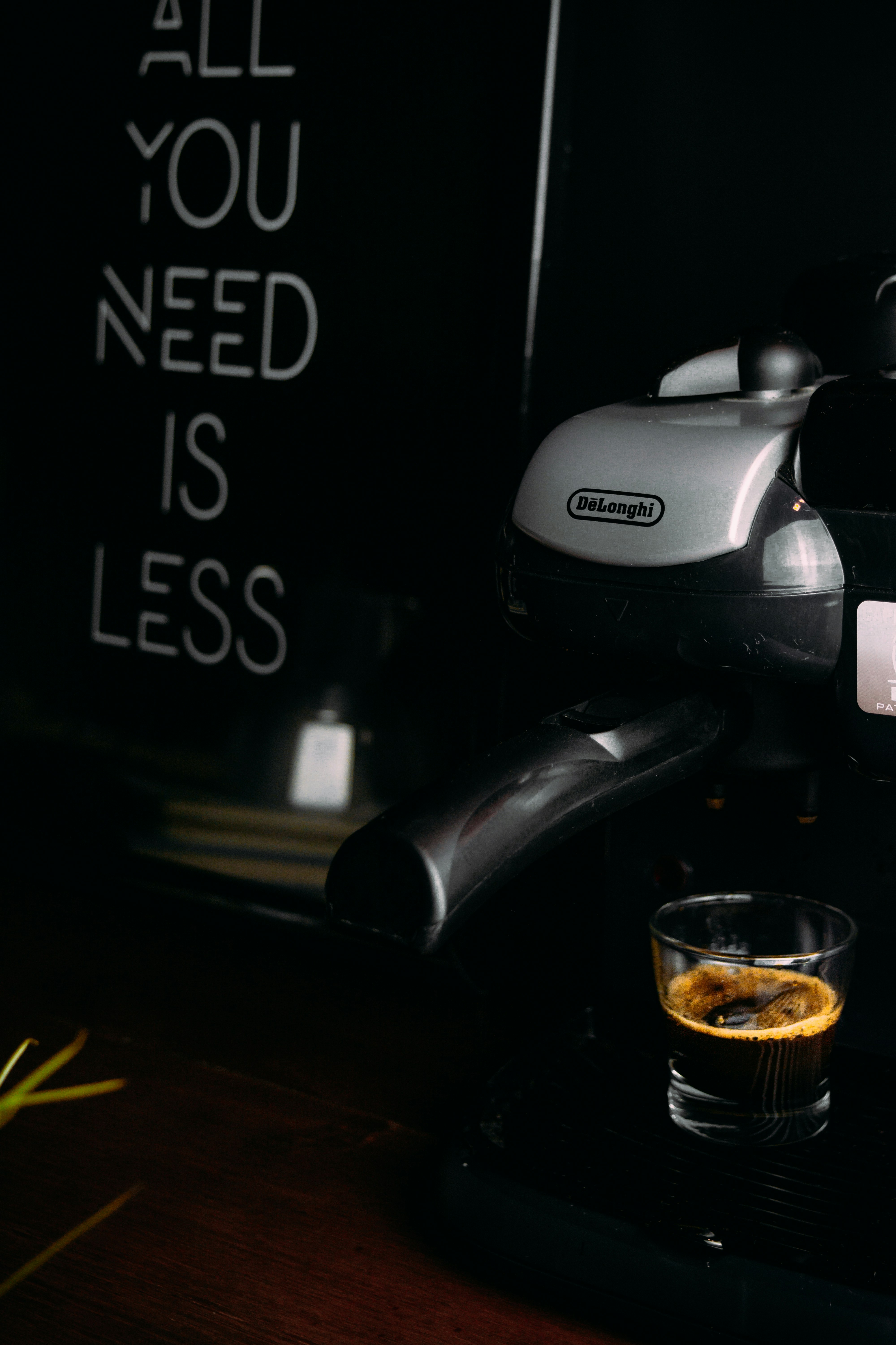 Midnight Espresso Moment: Delonghi on a Dim Counter Beneath a ‘Less’ Motto