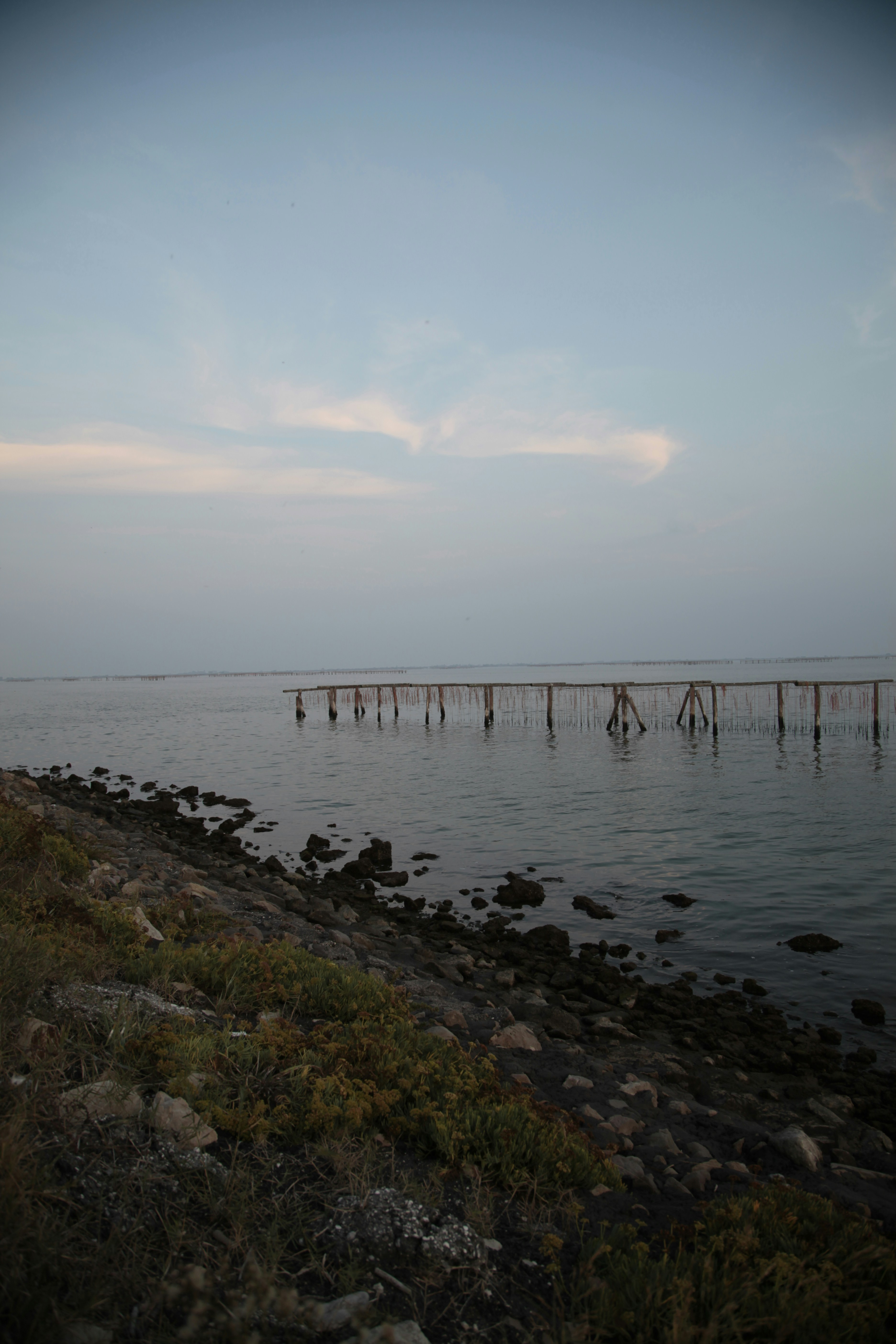 Rocky shoreline leading to a weathered pier under a serene evening sky.