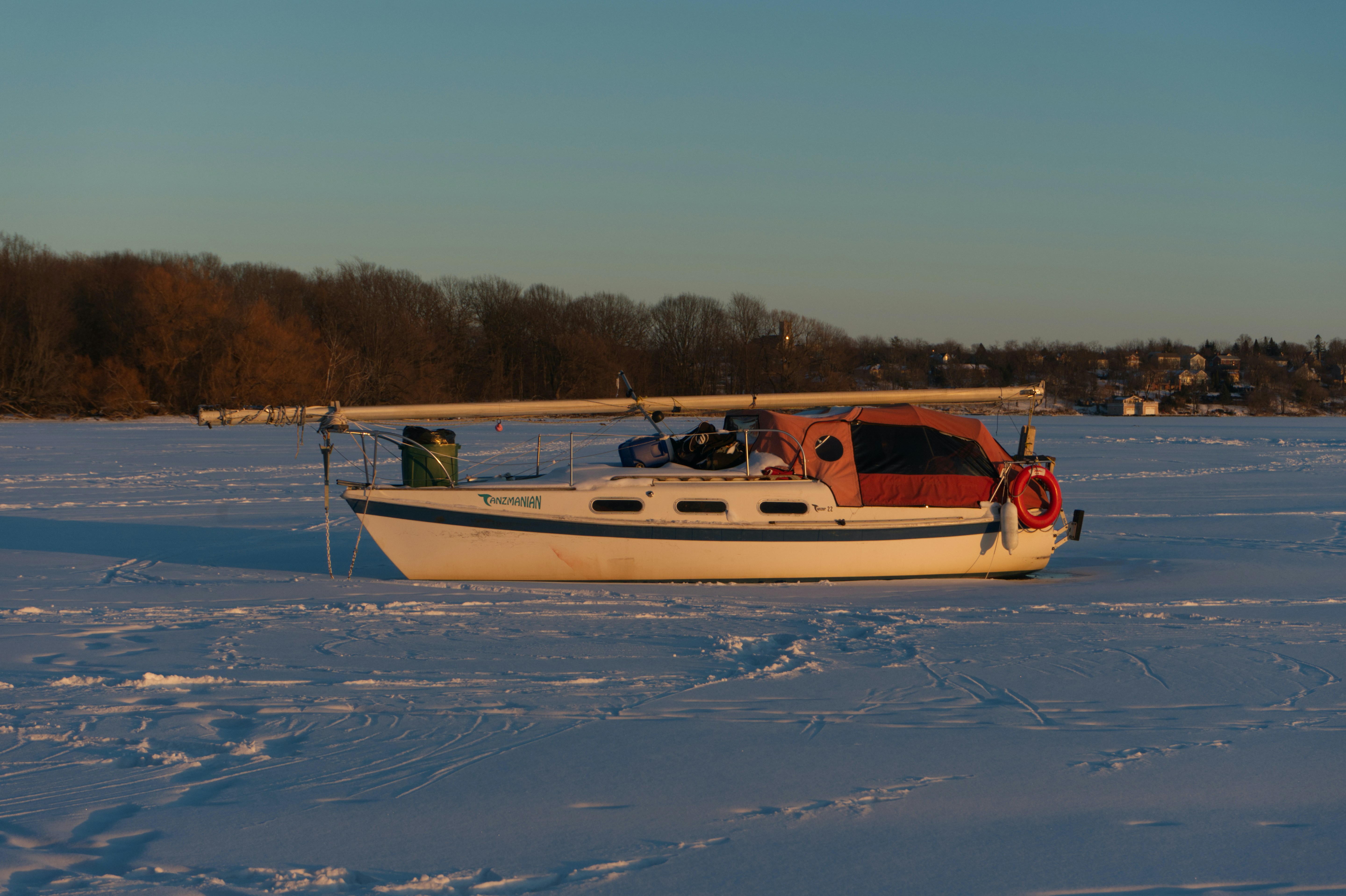 A sailboat rests peacefully on a frozen landscape, surrounded by untouched snow and a clear blue sky. The scene captures the stillness of winter's embrace.