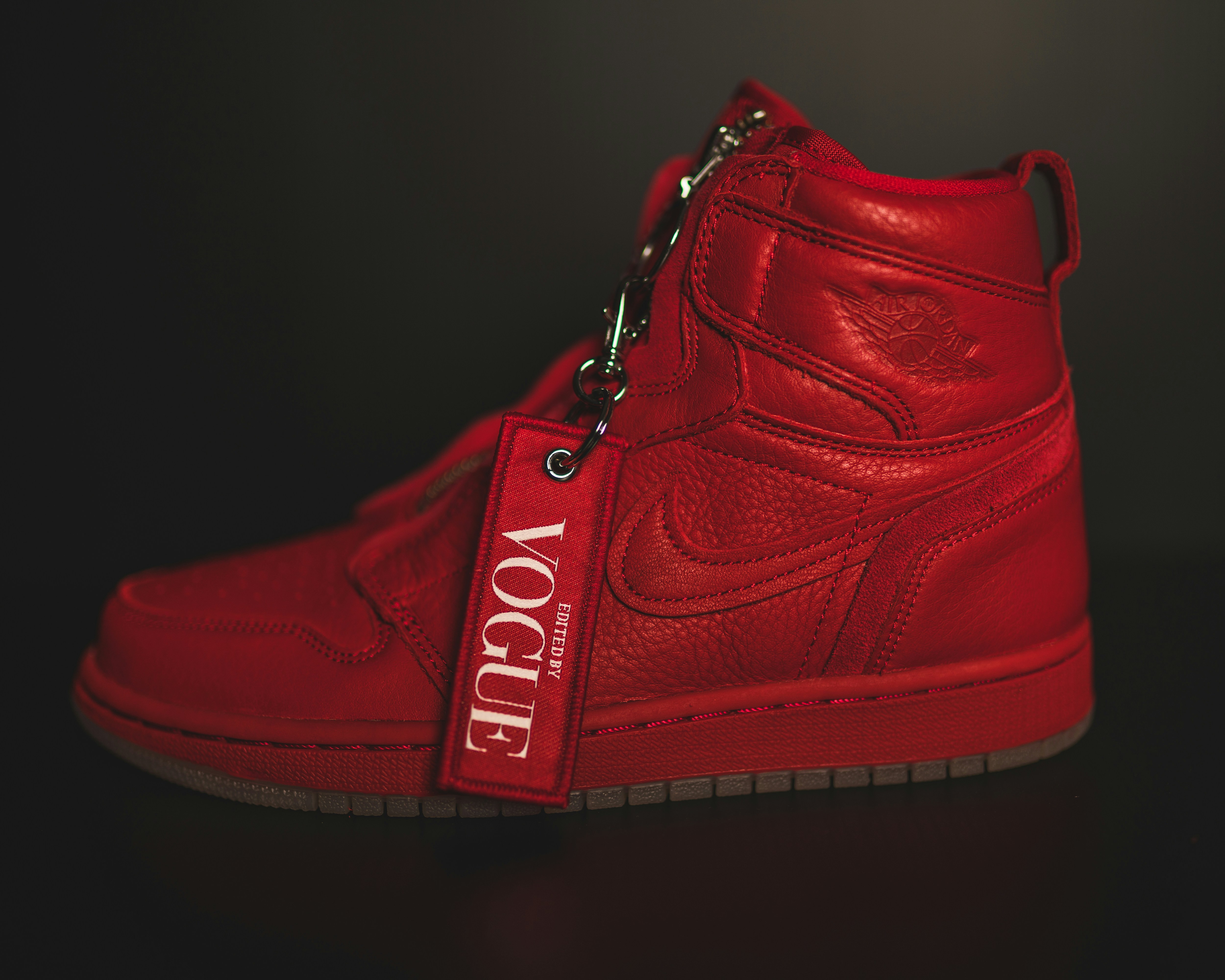A striking red sneaker featuring a prominent 'VOGUE' tag, showcasing its stylish design against a dark background.