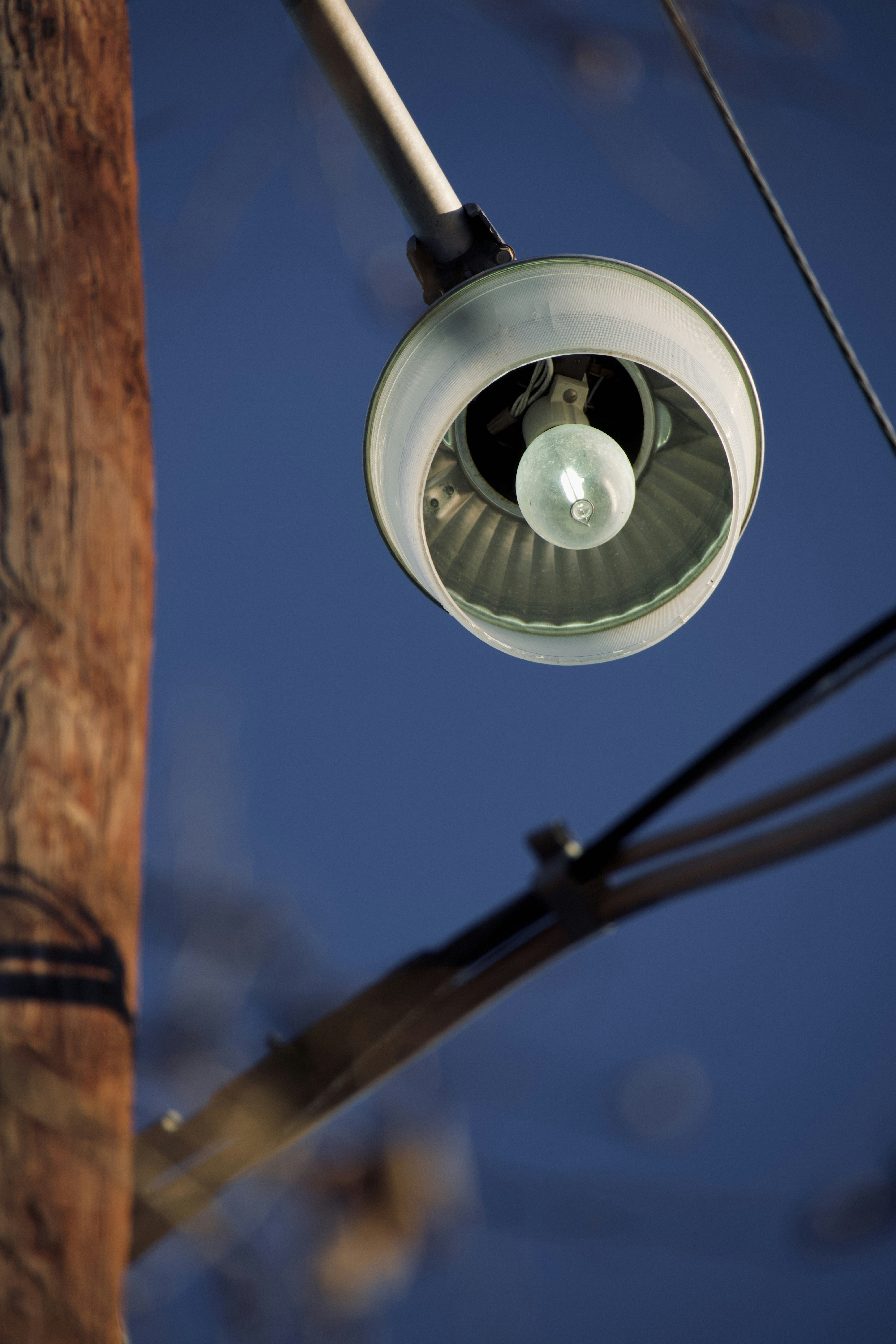 Vintage street lamp hanging from a utility pole against a clear blue sky.