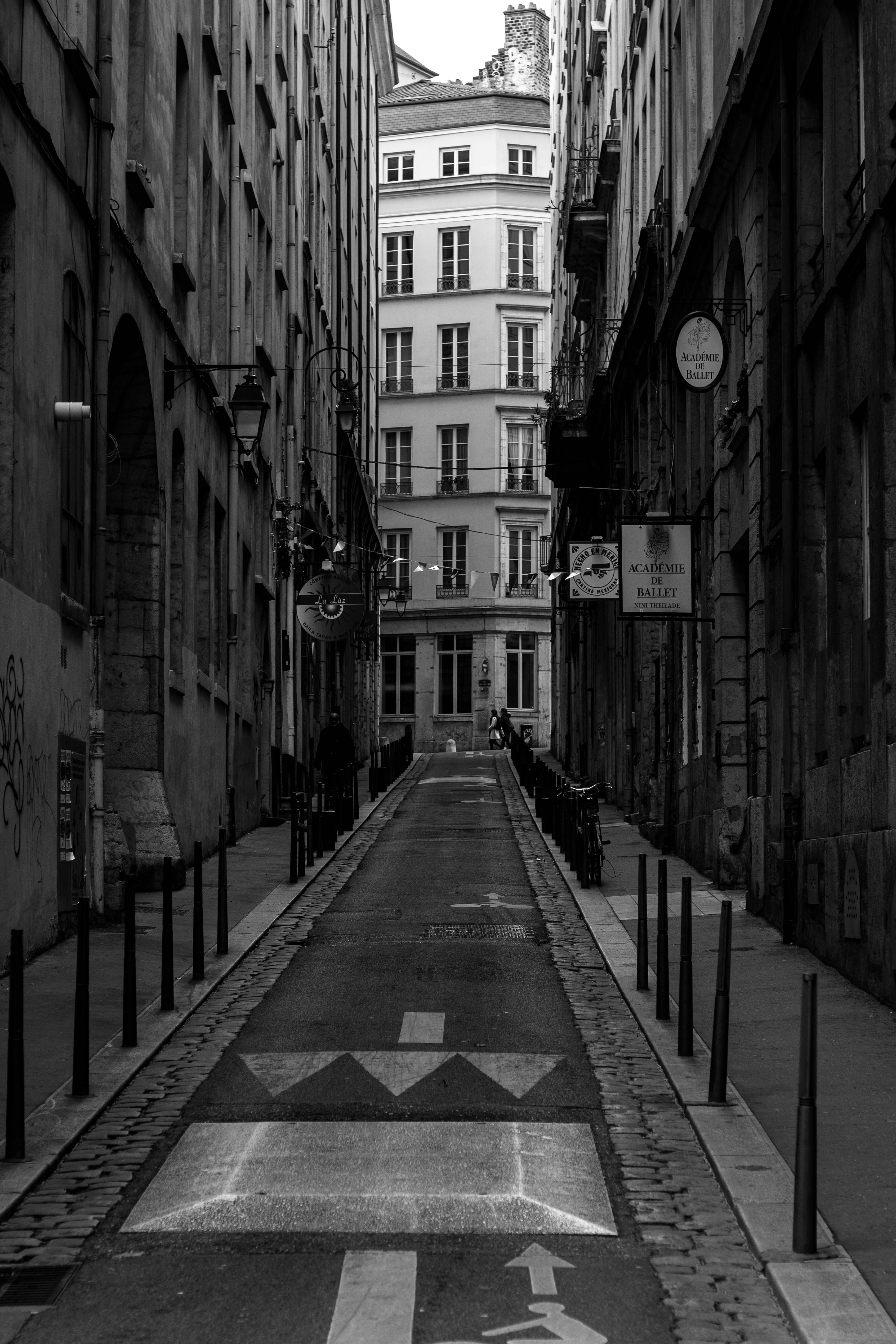 Narrow Parisian alleyway leading to a distant building, framed by towering stone walls and subtle signage.