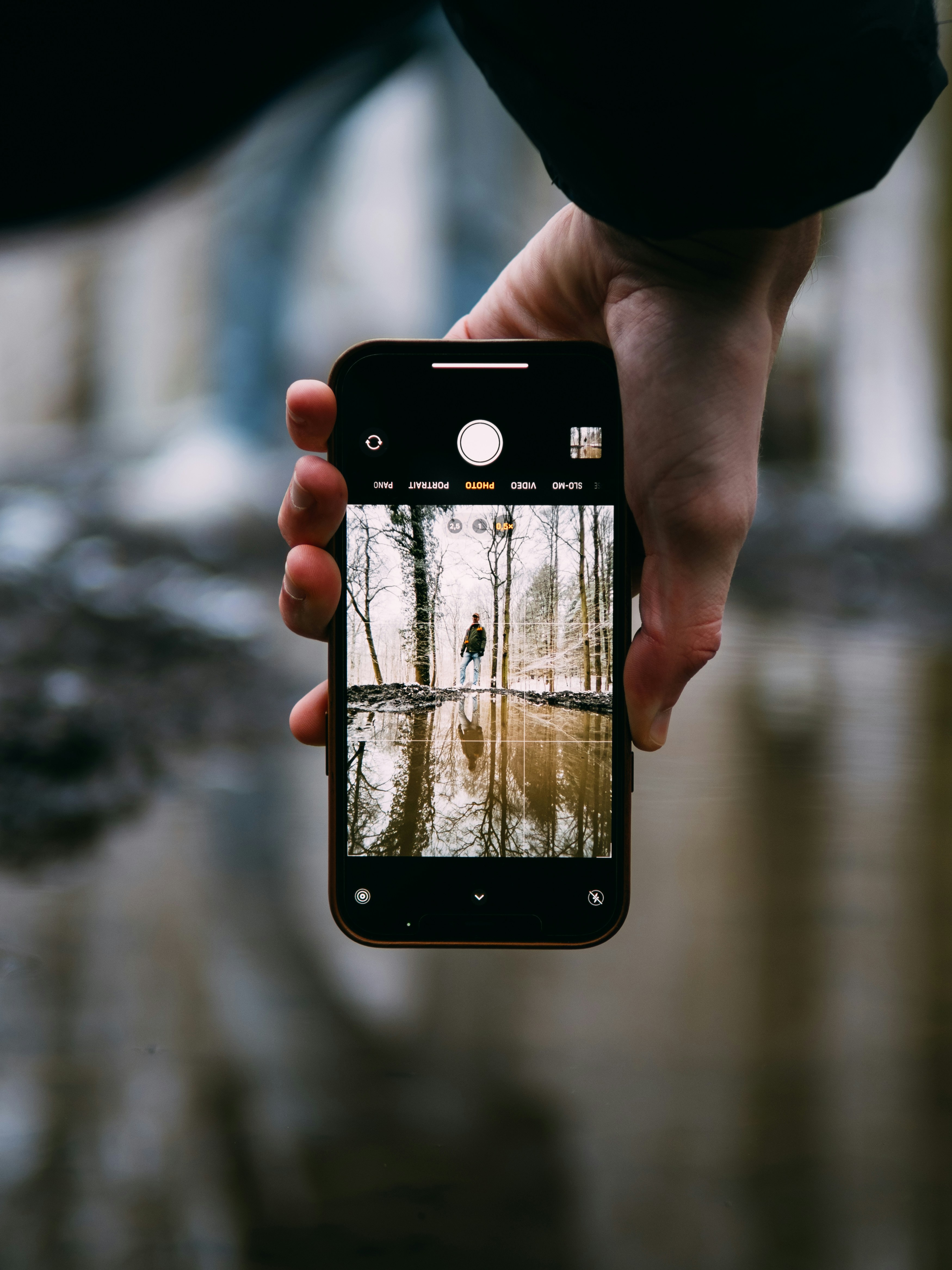 A hand holds a smartphone displaying a serene forest scene with reflections in water. The image emphasizes the connection between technology and the natural world.