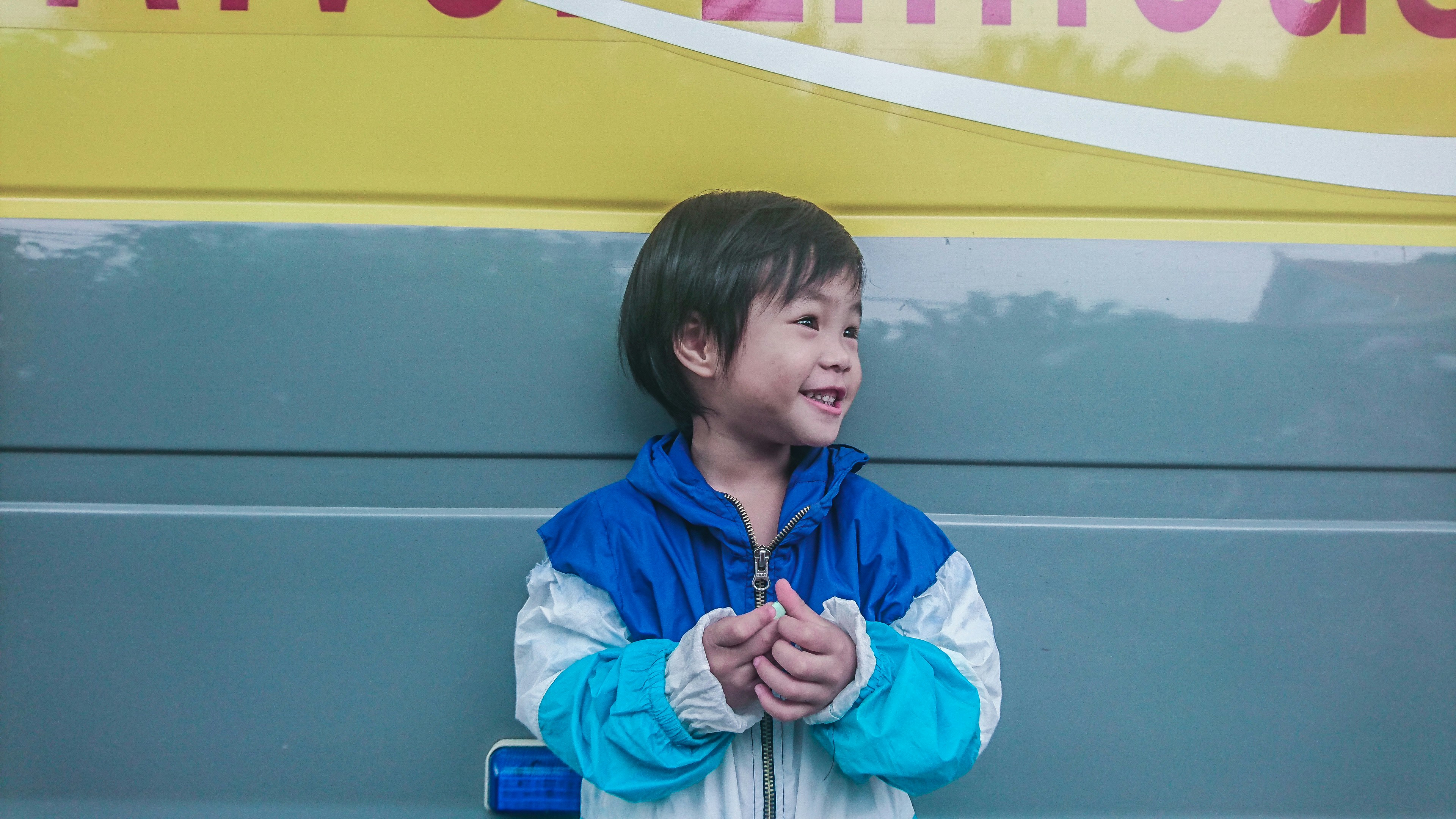 Child smiling joyfully while standing against a colorful van backdrop.