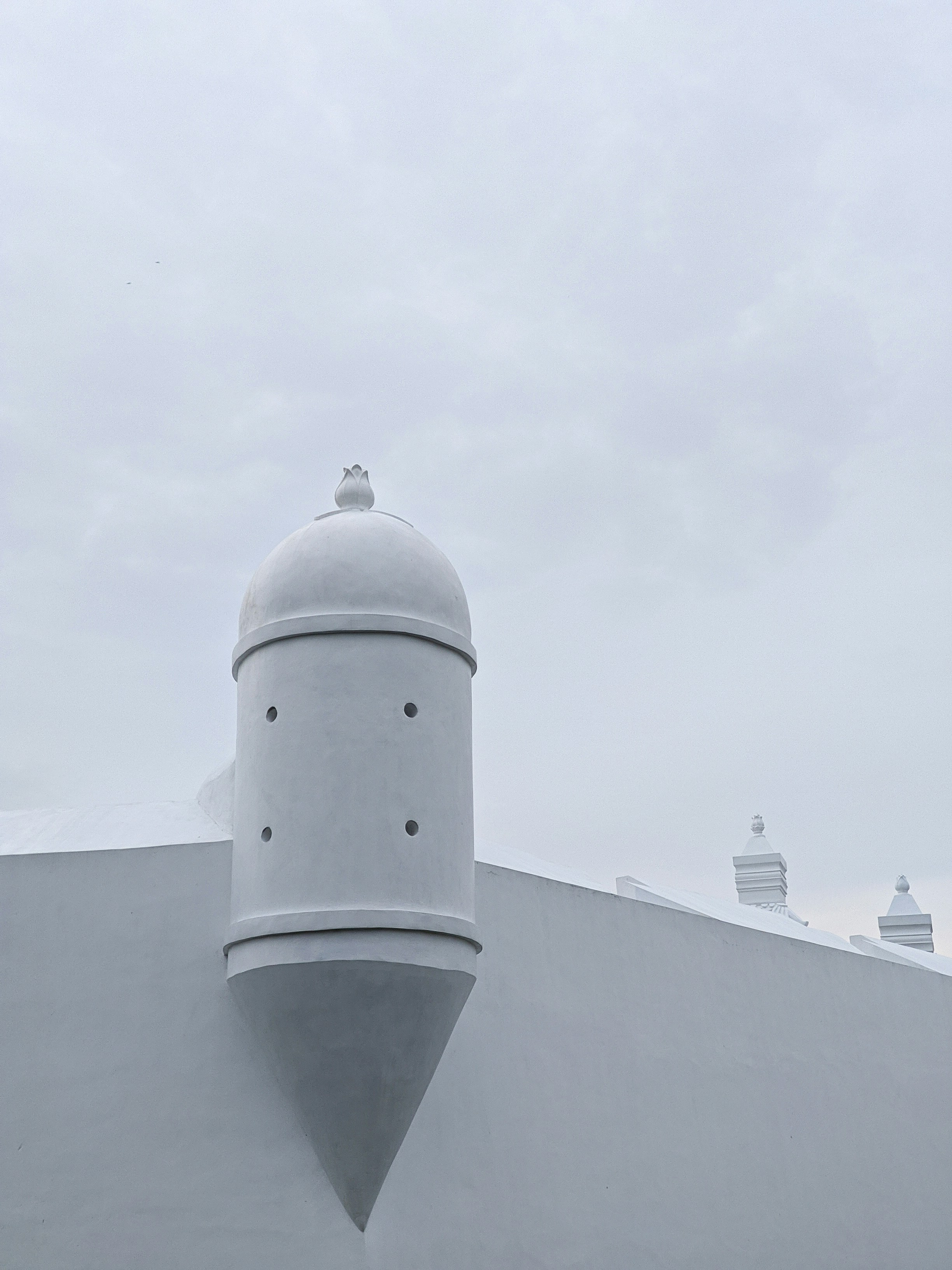 A white architectural feature stands against a cloudy sky, showcasing a blend of traditional design and modern minimalism.